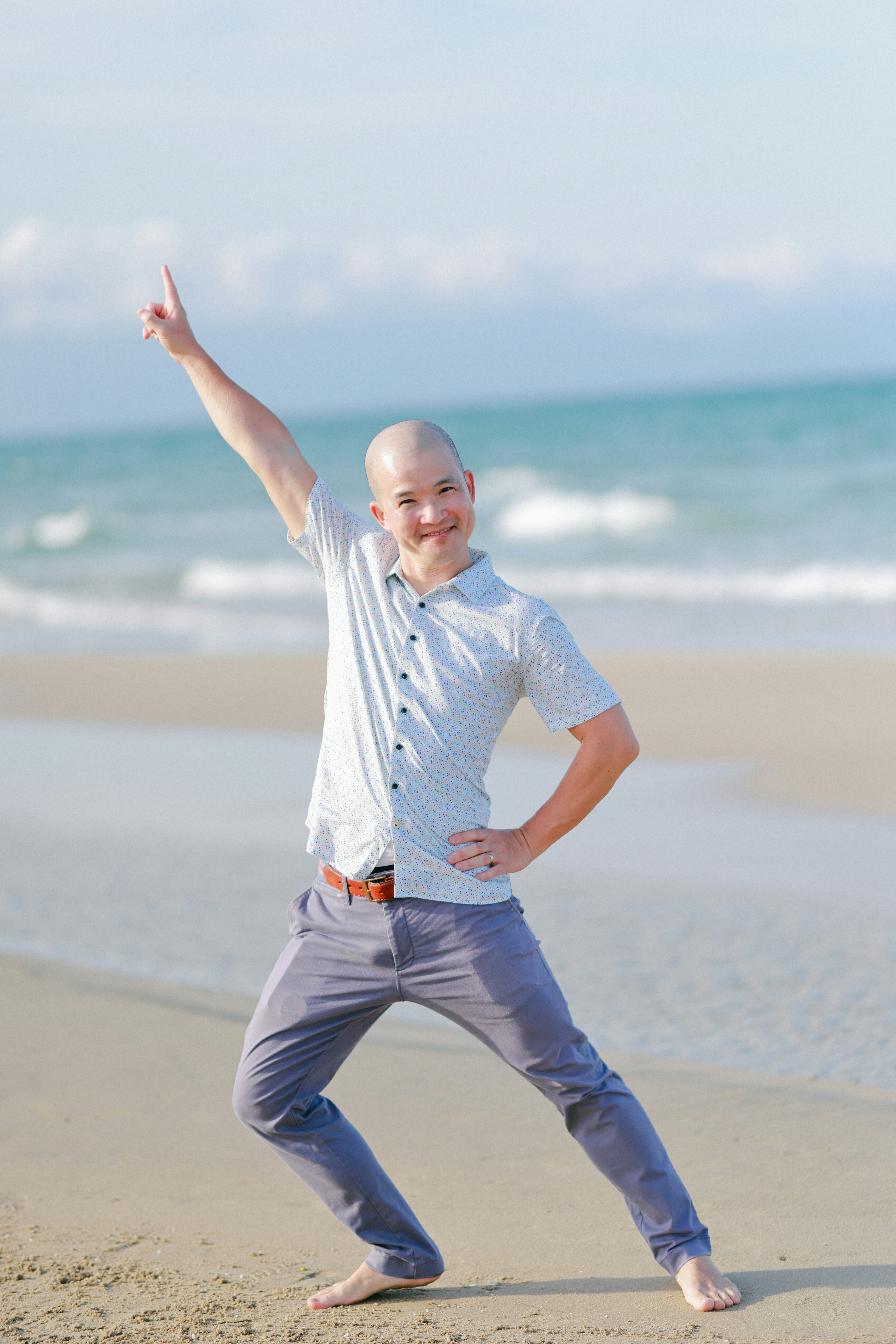 Joyful Beach Pose: Man in White Shirt Points Skyward