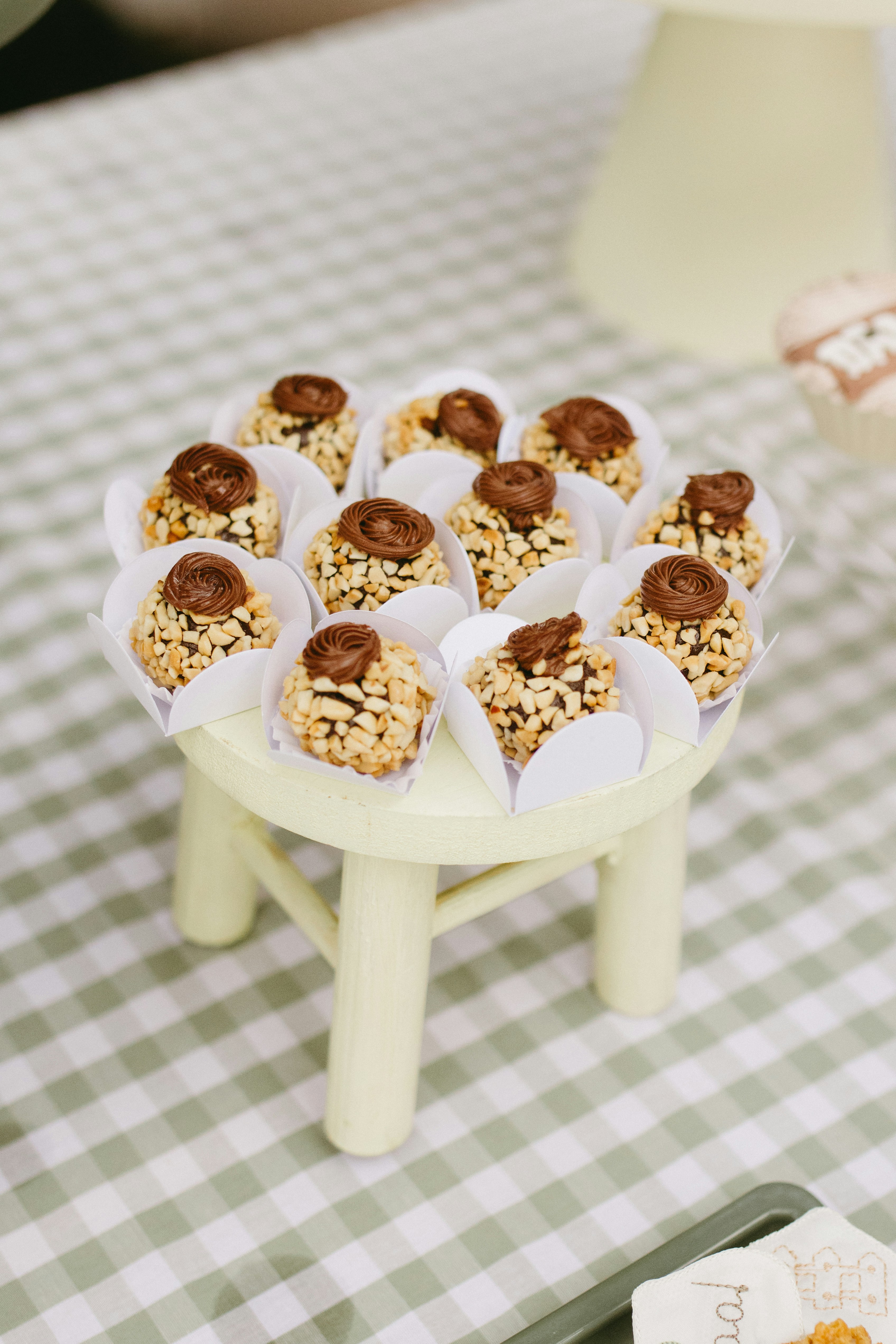 Assorted chocolate truffles with toasted hazelnuts arranged on a pale yellow stand atop a checkered tablecloth.
