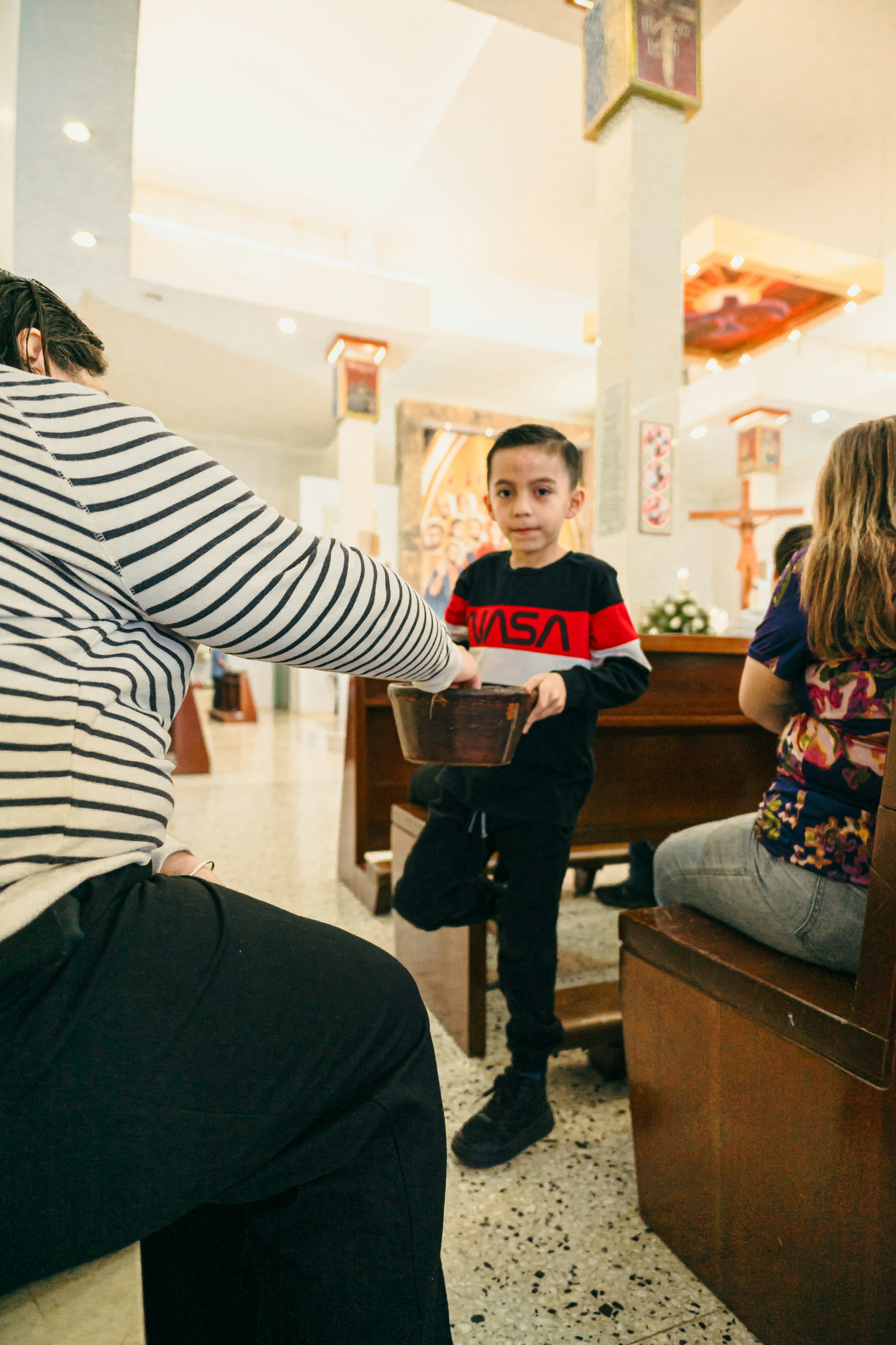 A Shared Moment: Child Reaches for a Wooden Bowl in a Quiet Church Corridor