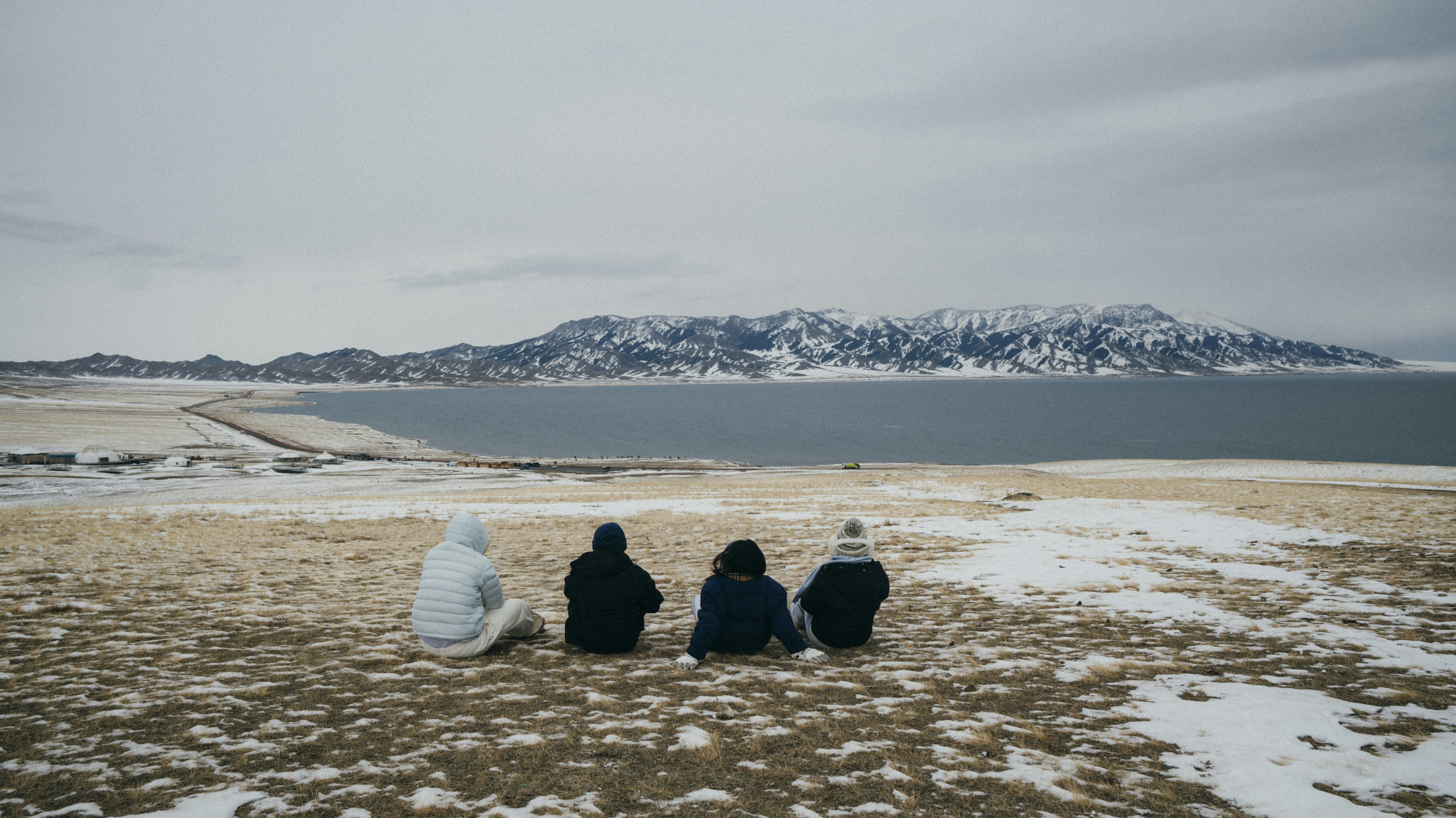 Quiet Circle by the Shore: Four Figures on Snow-Dusted Beach