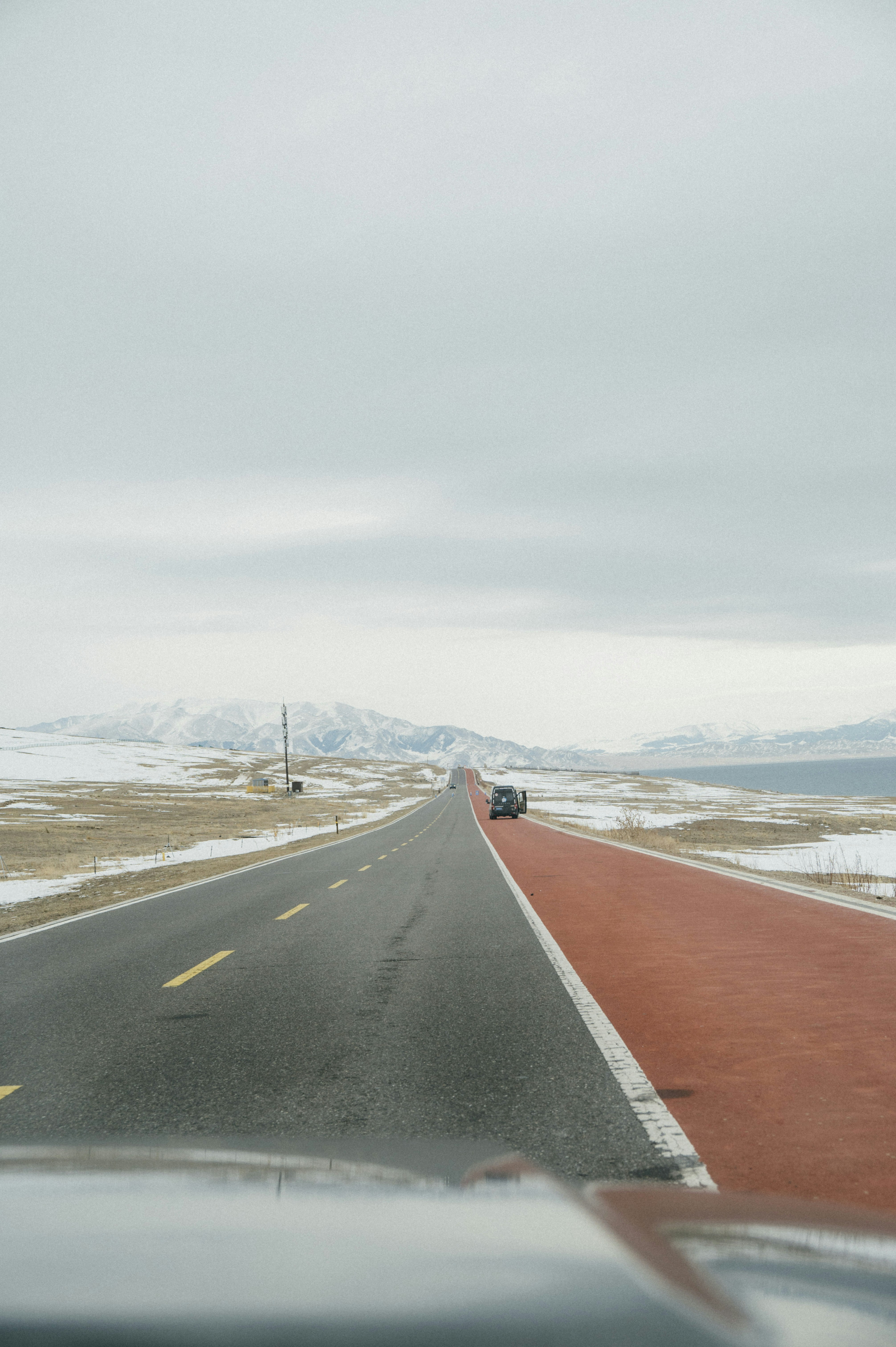 Long Road to Winter: A Red Ribbon of Asphalt Through Snow-kissed Plains