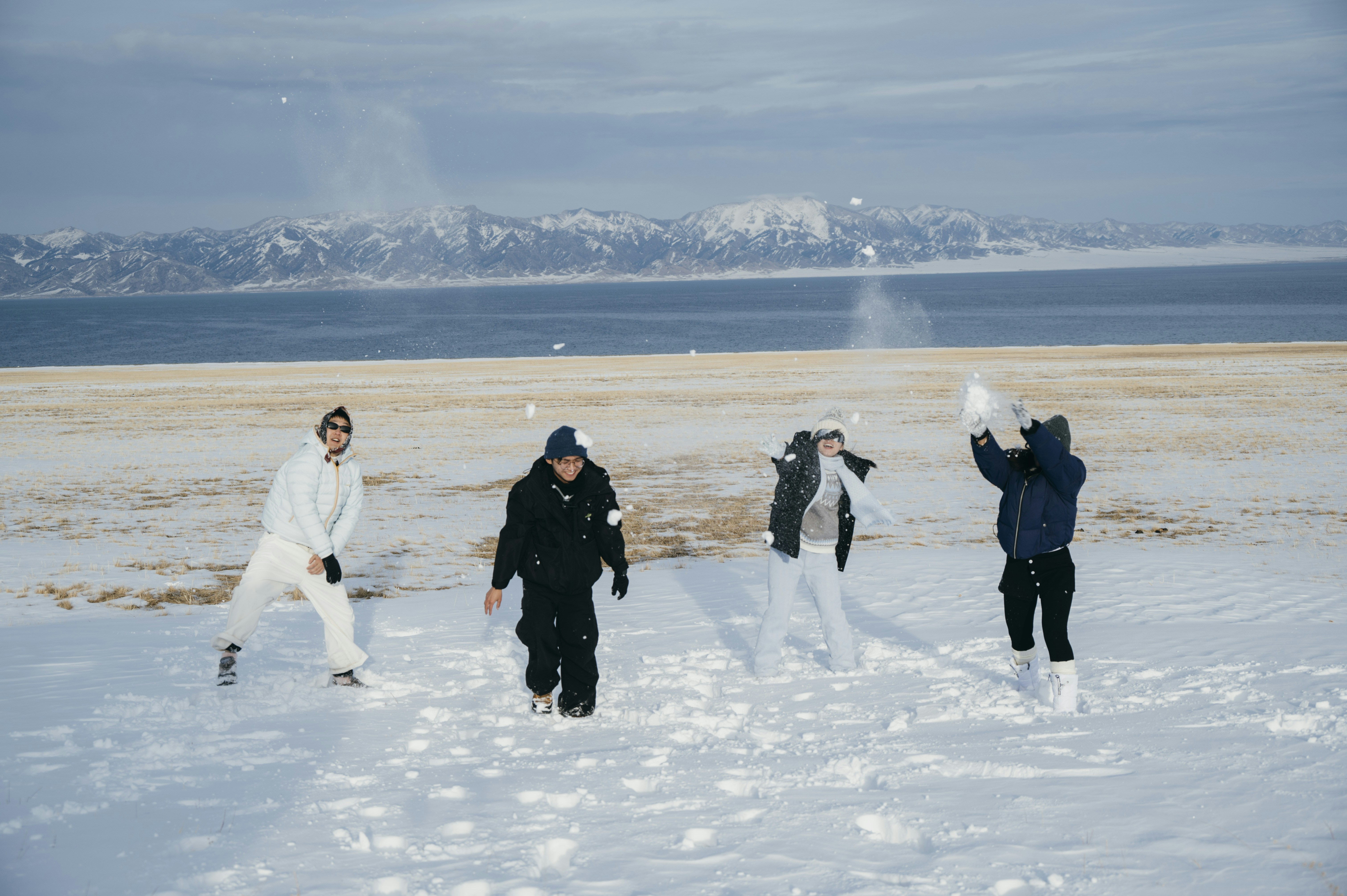 Snowy Club: Friends Tossing Snow in a Wide Lakeside Field