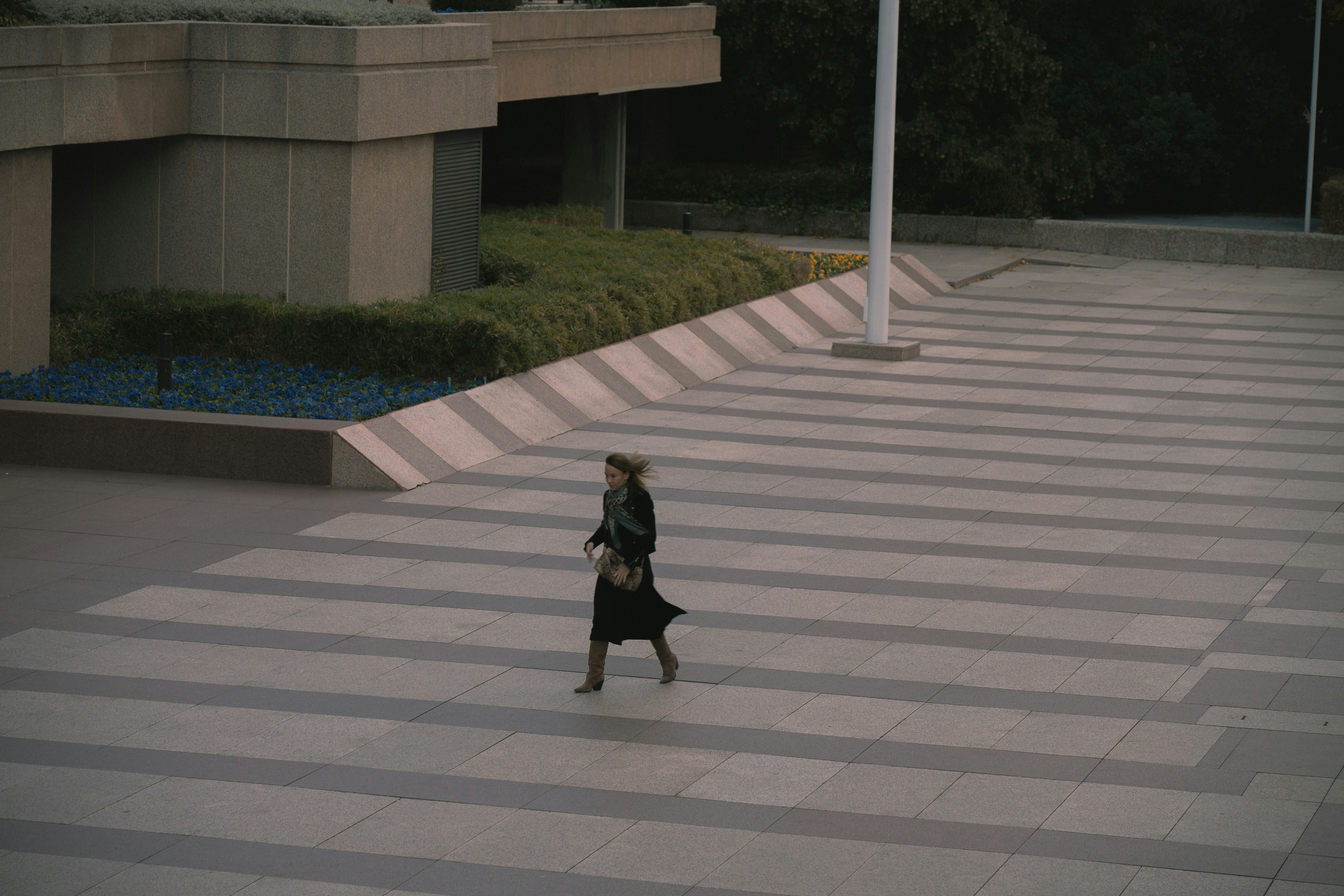 Solo commuter crosses geometric plaza under muted daylight