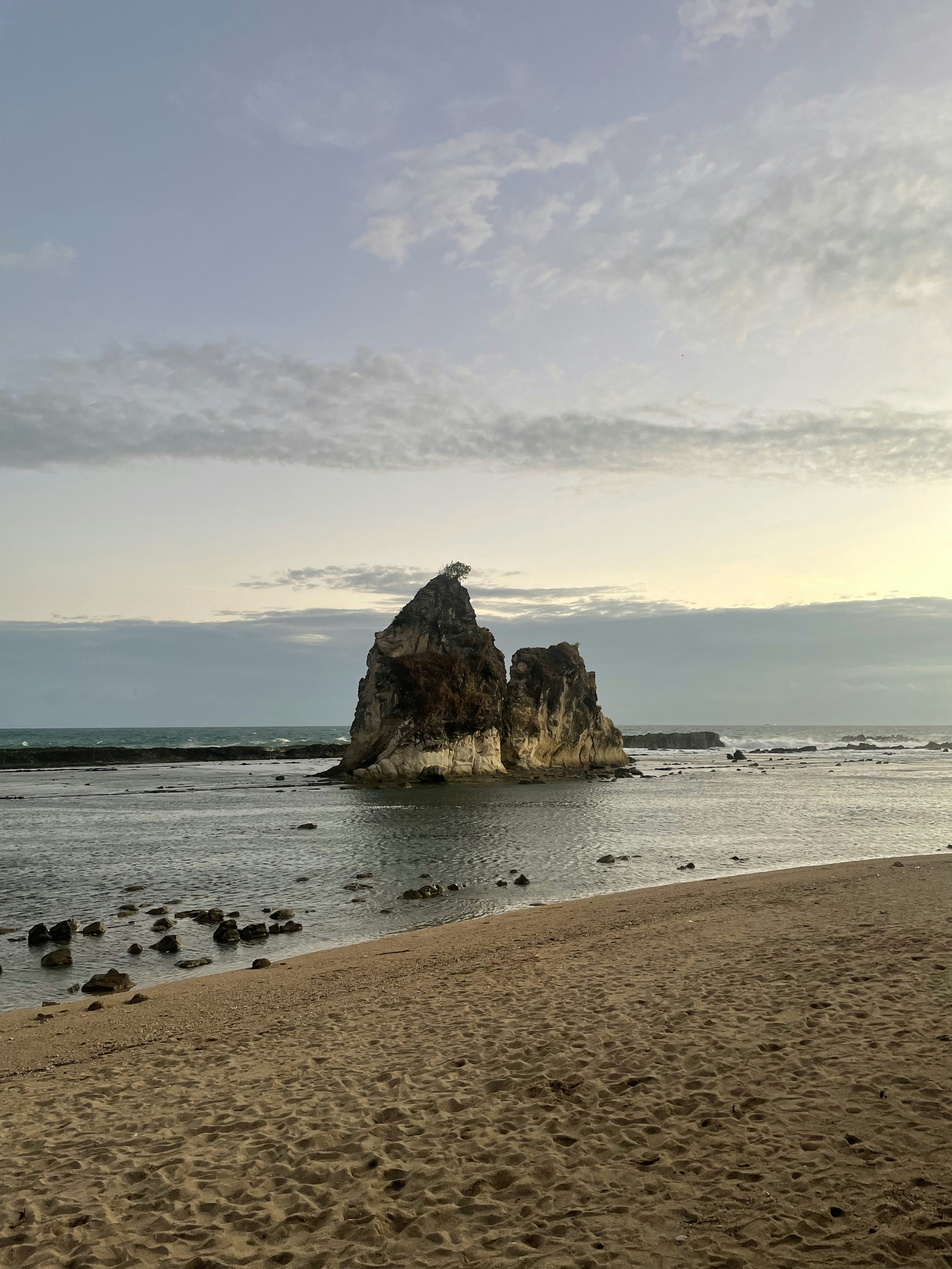 Coastal Monument: A Sea Stack Rising from Quiet Sands at Sunset