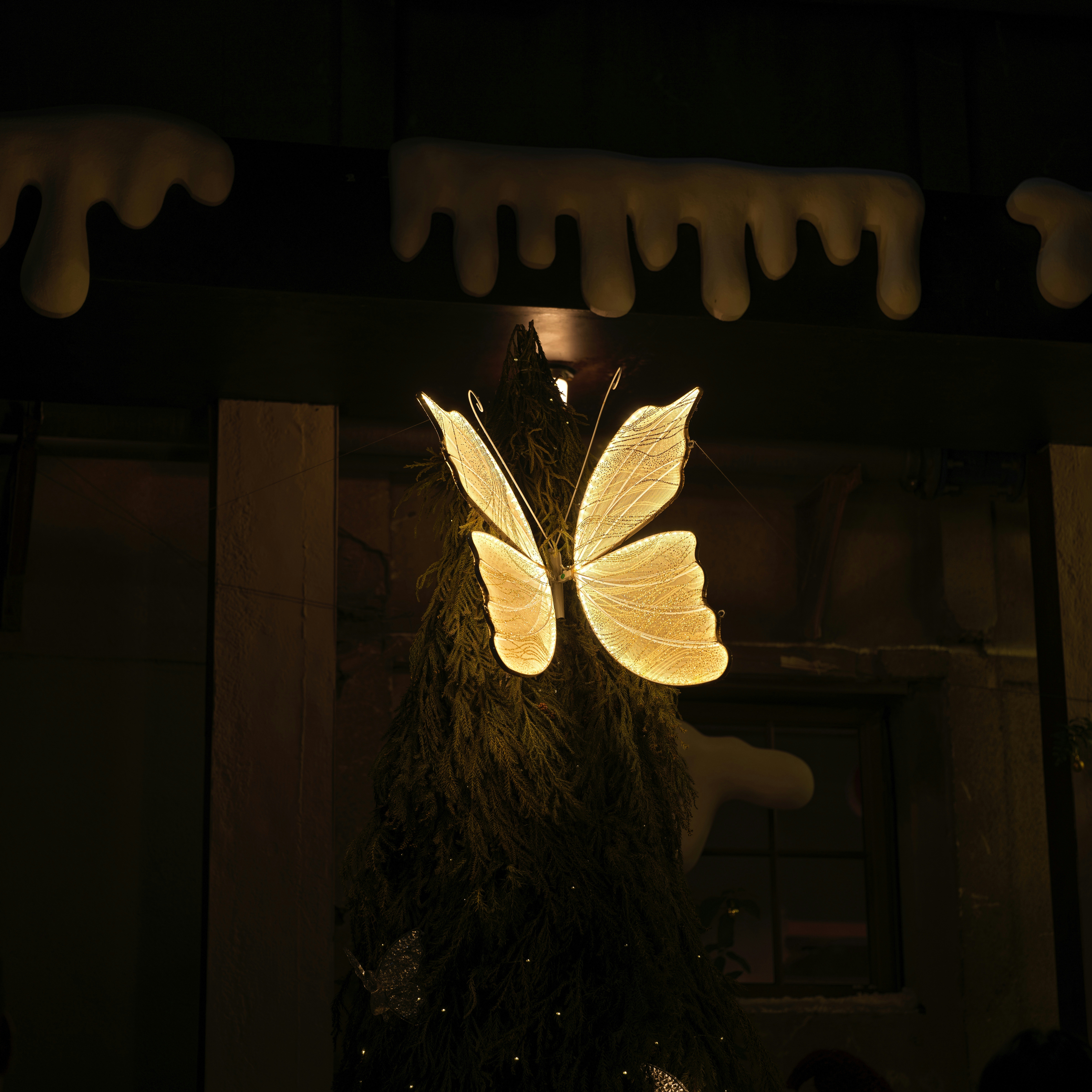 Glowing butterfly decoration atop a dark christmas tree
