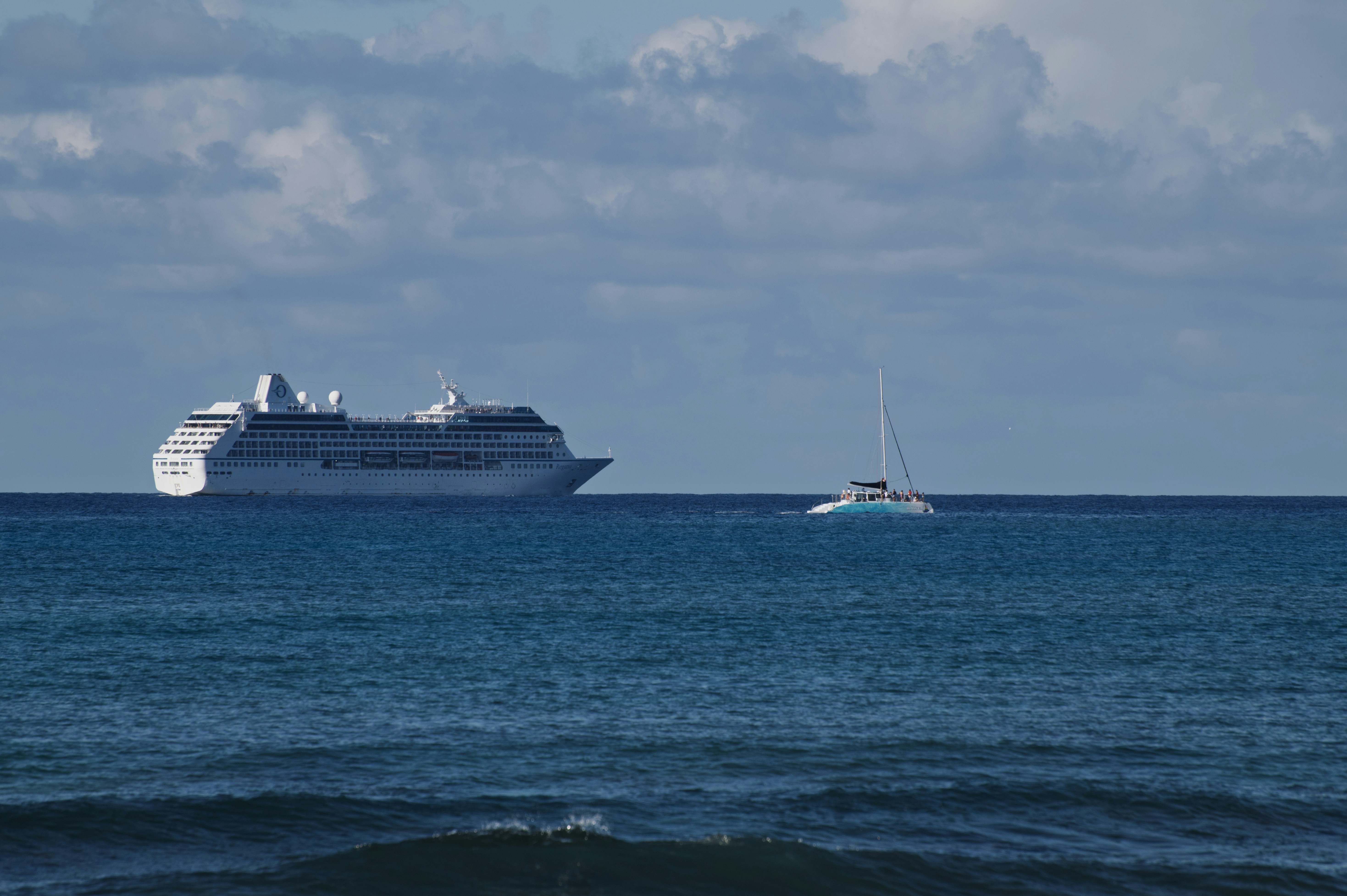 A large cruise ship and sailboat on the ocean.