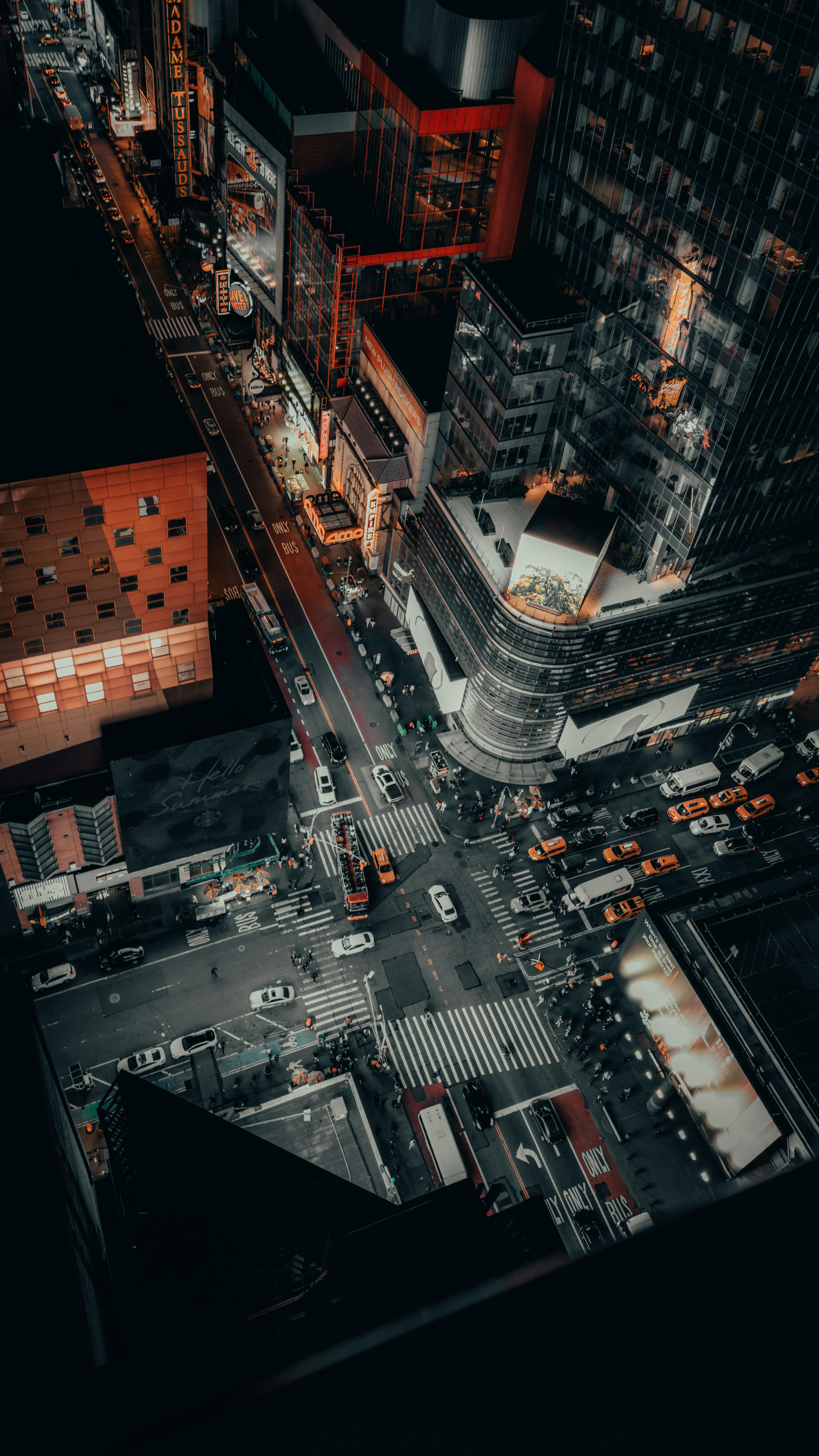 A cinematic, high-angle view of Times Square in New York City at night, with glowing billboards, dense crowds, and streams of traffic and yellow taxis cutting through the intersection below.