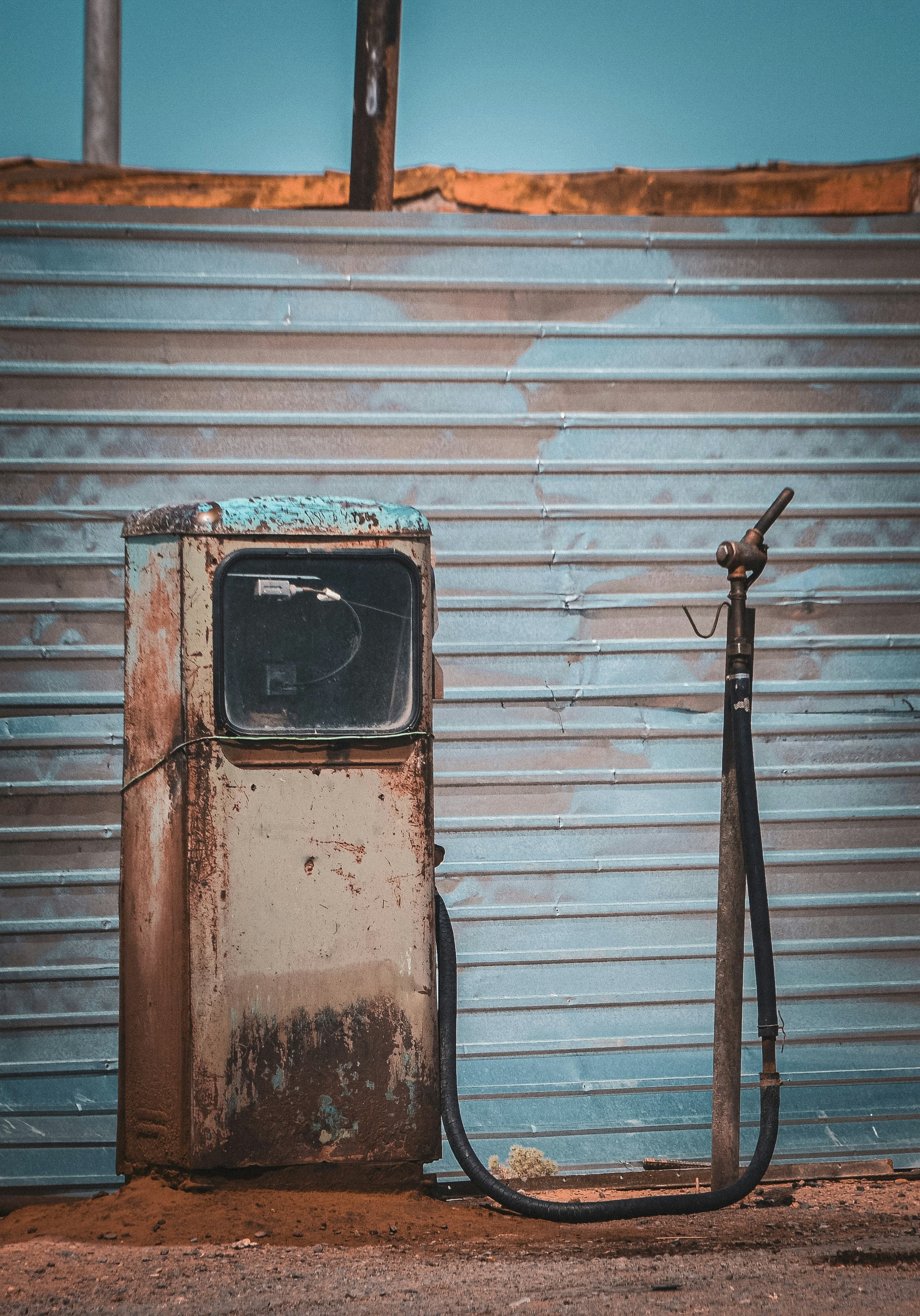 An old rusted gas pump stands against a faded blue corrugated wall, its peeling paint and weathered textures telling a story of time and abandonment.