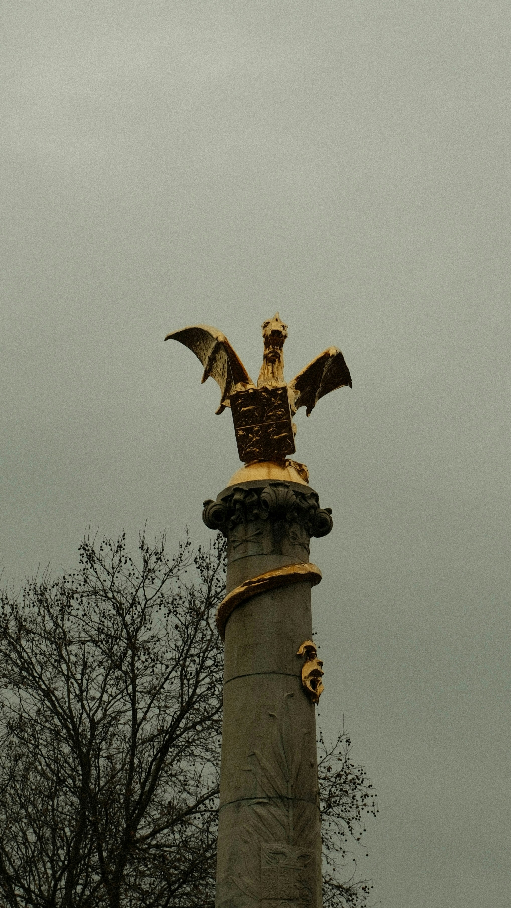 Golden dragon statue atop a column against cloudy sky.