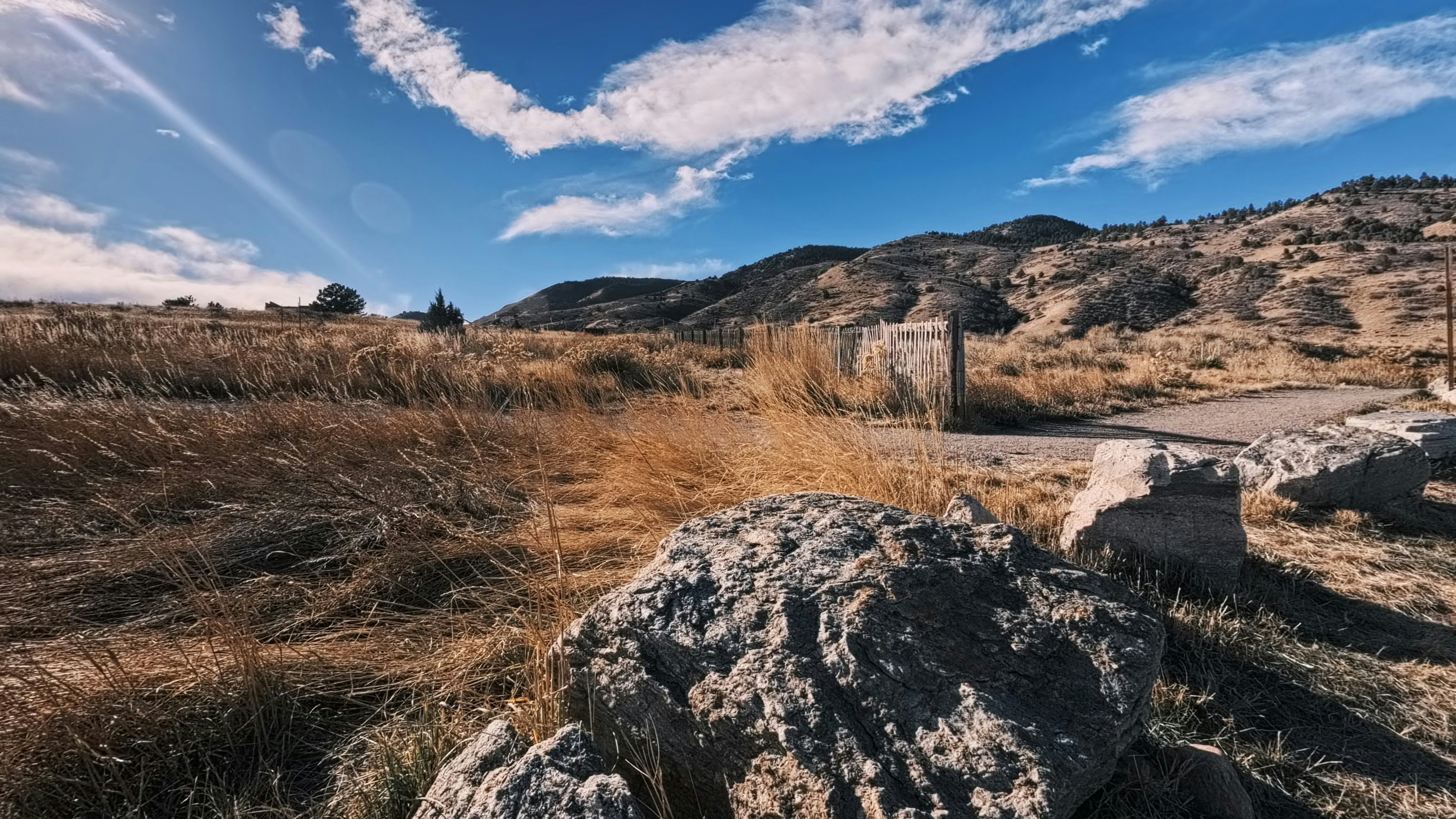 Dry grass and rocks with mountains under blue sky.