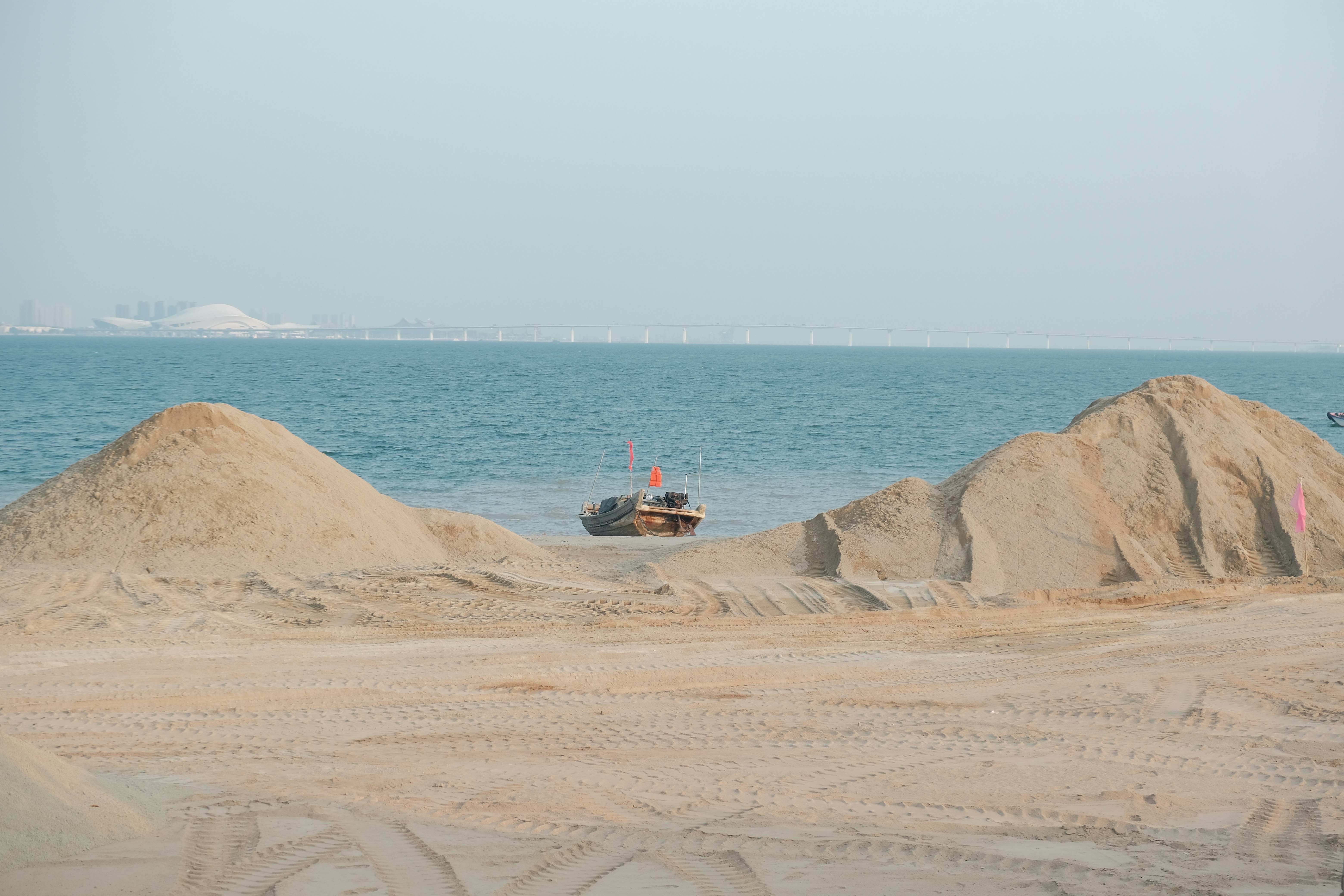 Quiet Construction on the Seashore: A Distant View of Sand Mounds and a Small Boat