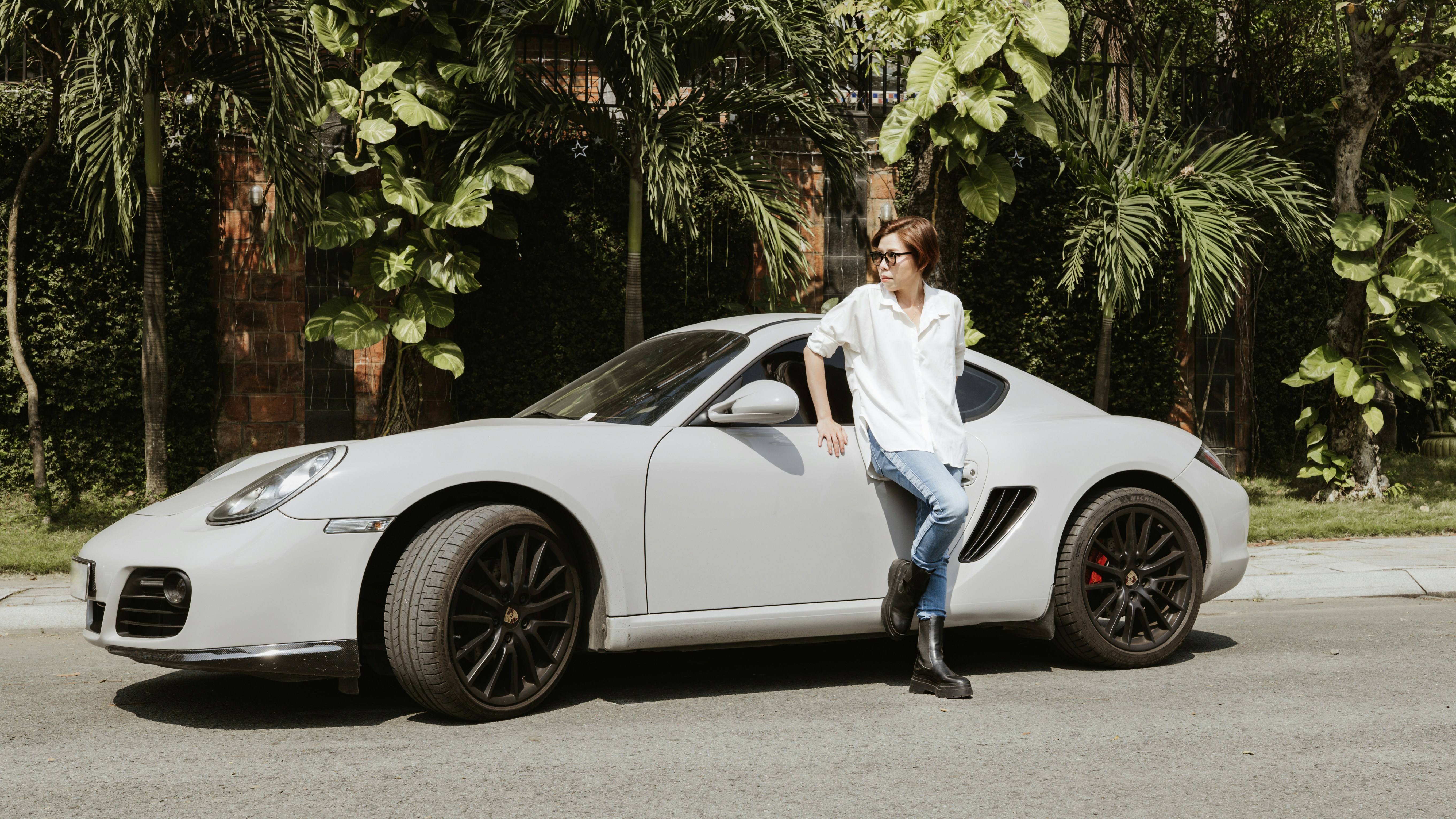 Sleek white Porsche against tropical backdrop with a casually posed figure
