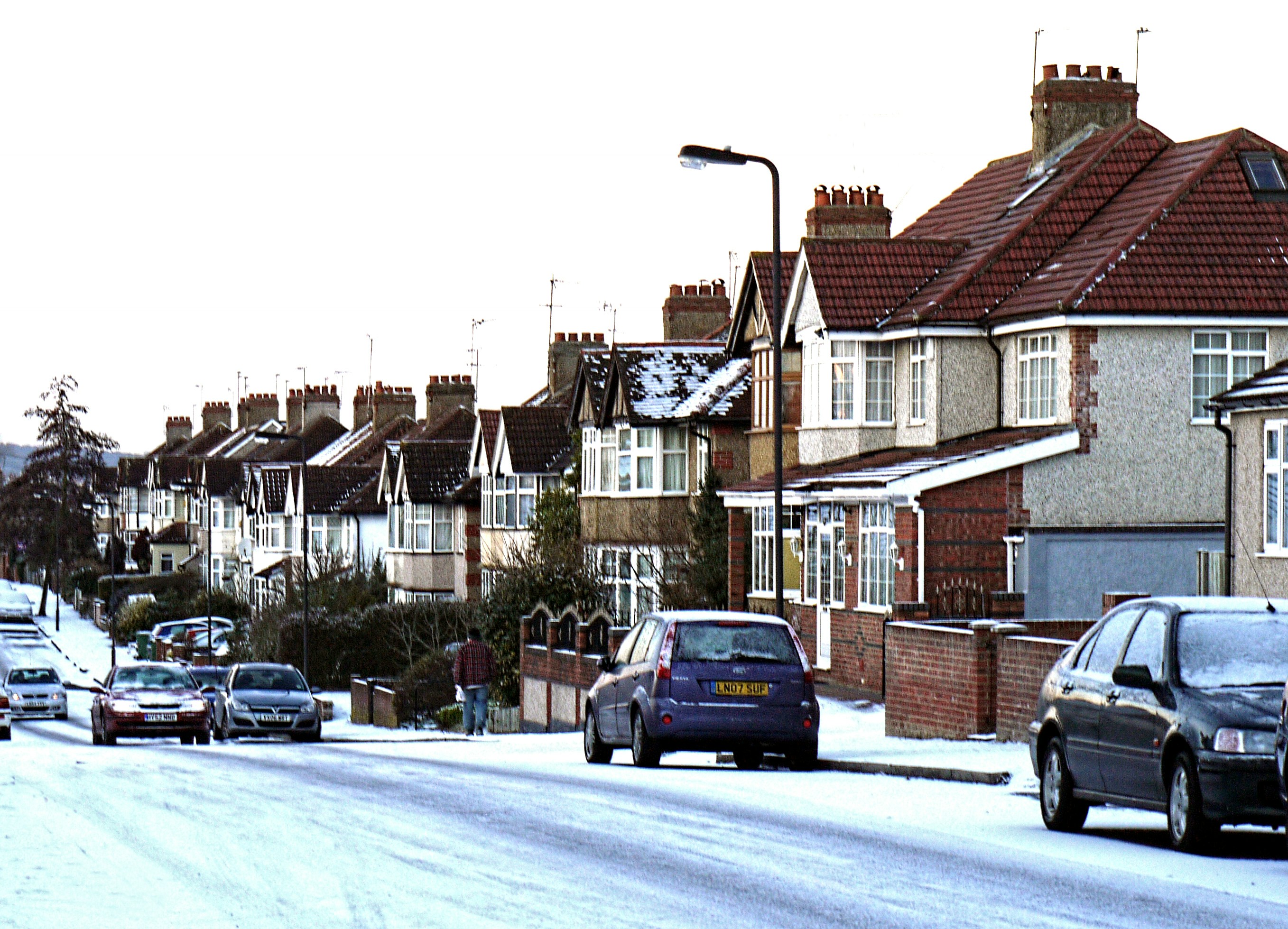 Snowy street lined with houses and cars.