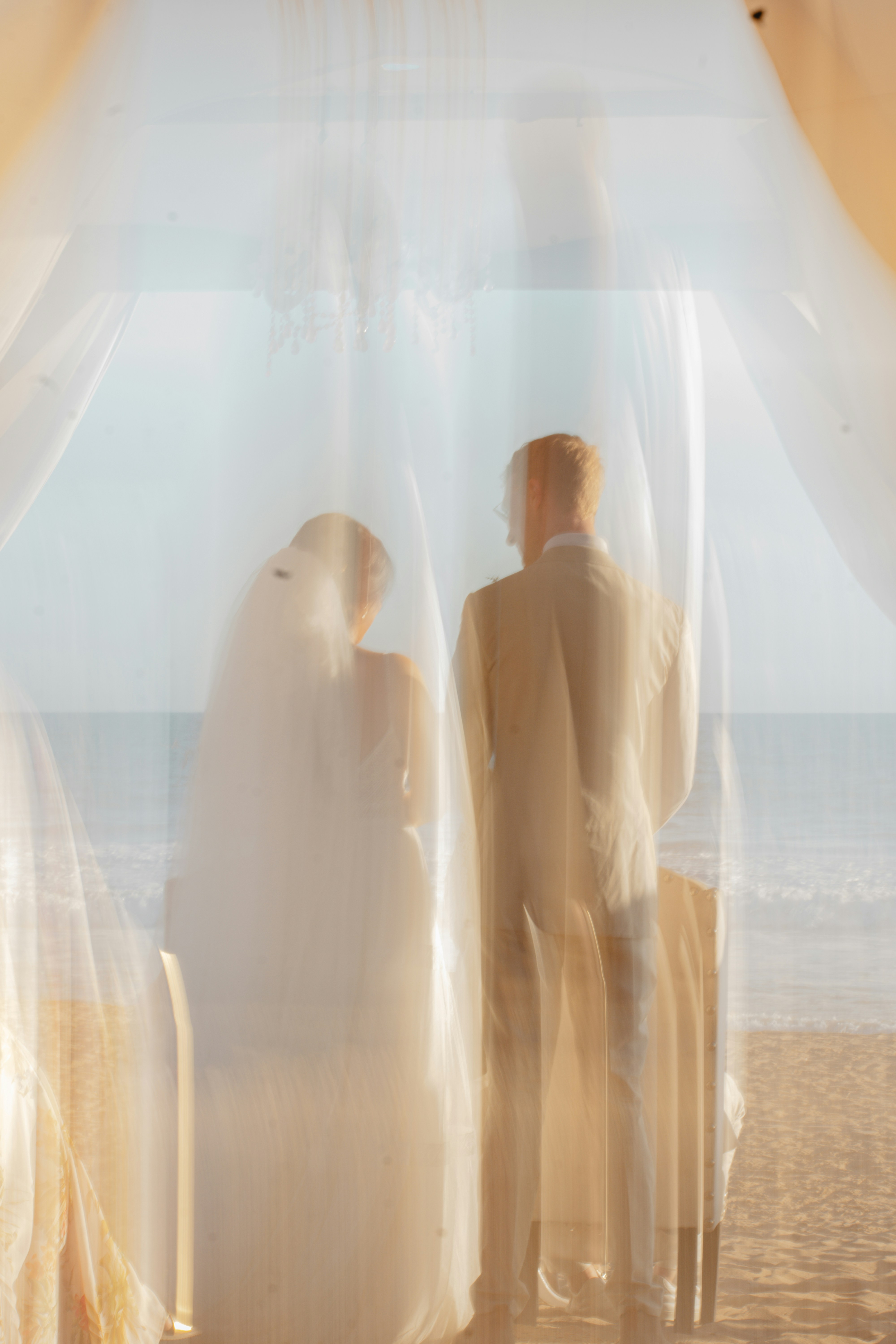 Veiled vows on the shoreline: two silhouettes beneath translucent curtains