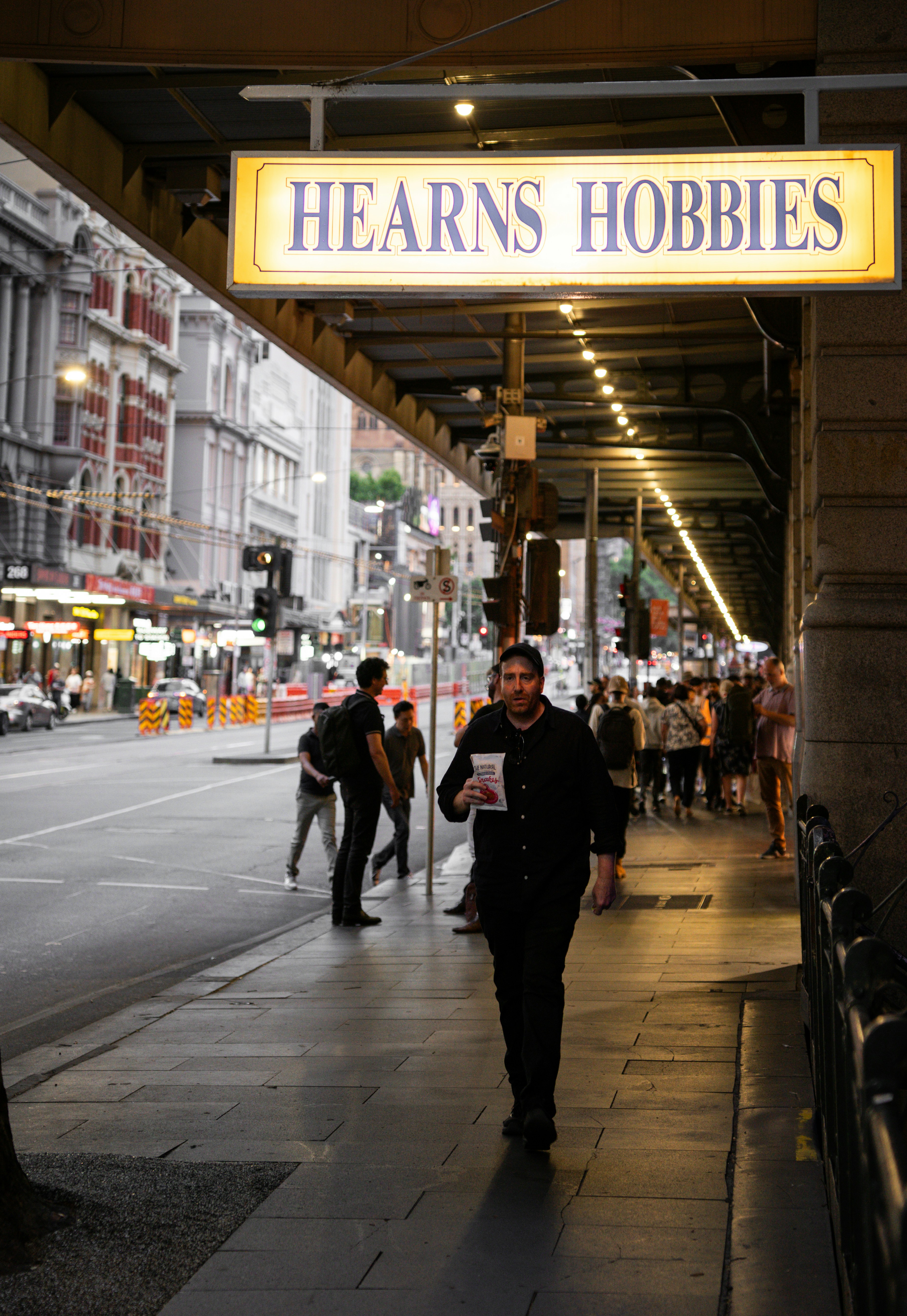 Under Neon Sign, Traveler Steps into the Evening Drift