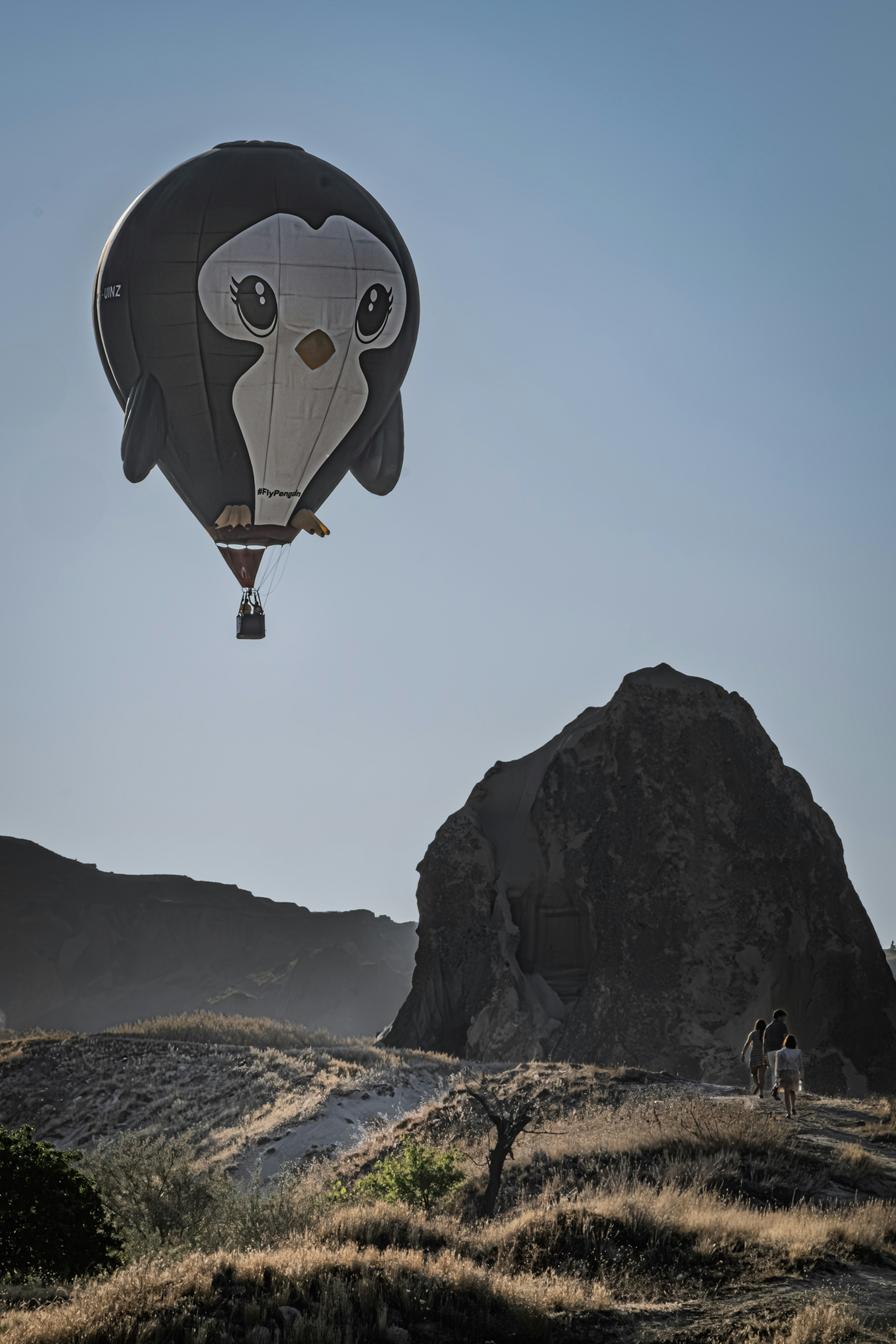 Penguin balloon drifts above a sunlit ridge as hikers approach a sea of rock