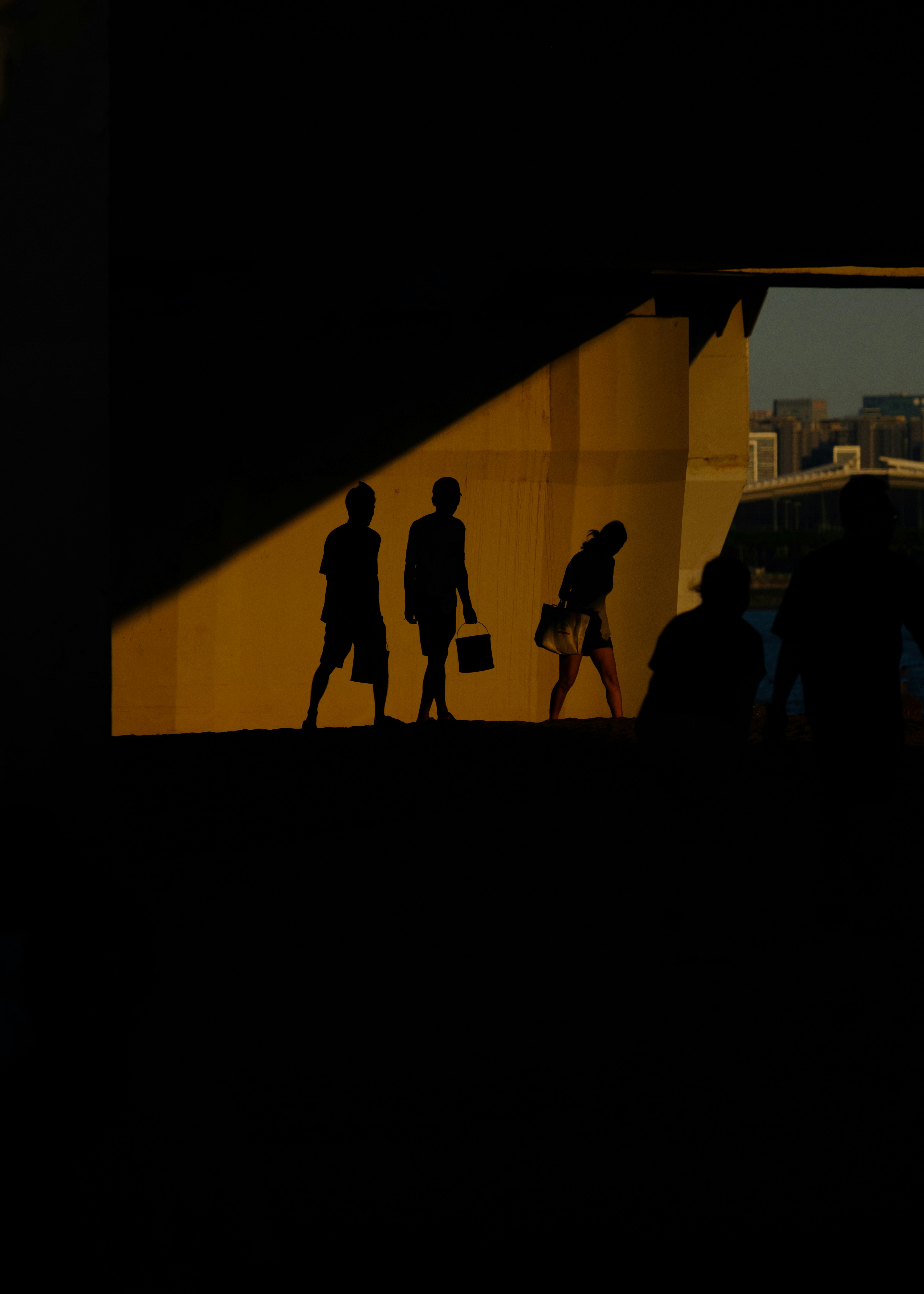Silhouetted Walkers in Golden Slant Under a City Bridge
