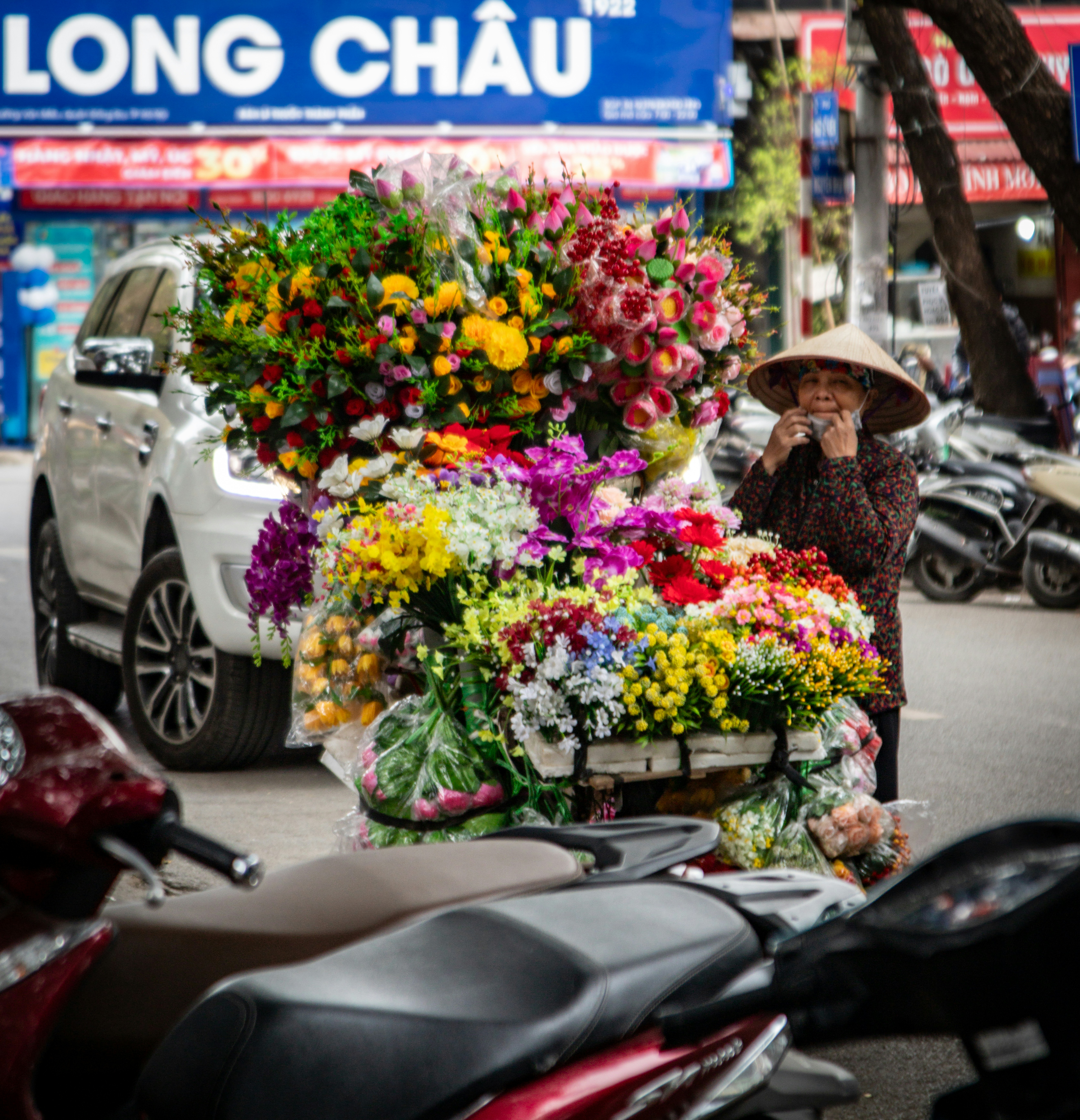 Bouquets on Wheels: A Flower Vendor Framed by a Bustling Vietnamese Street