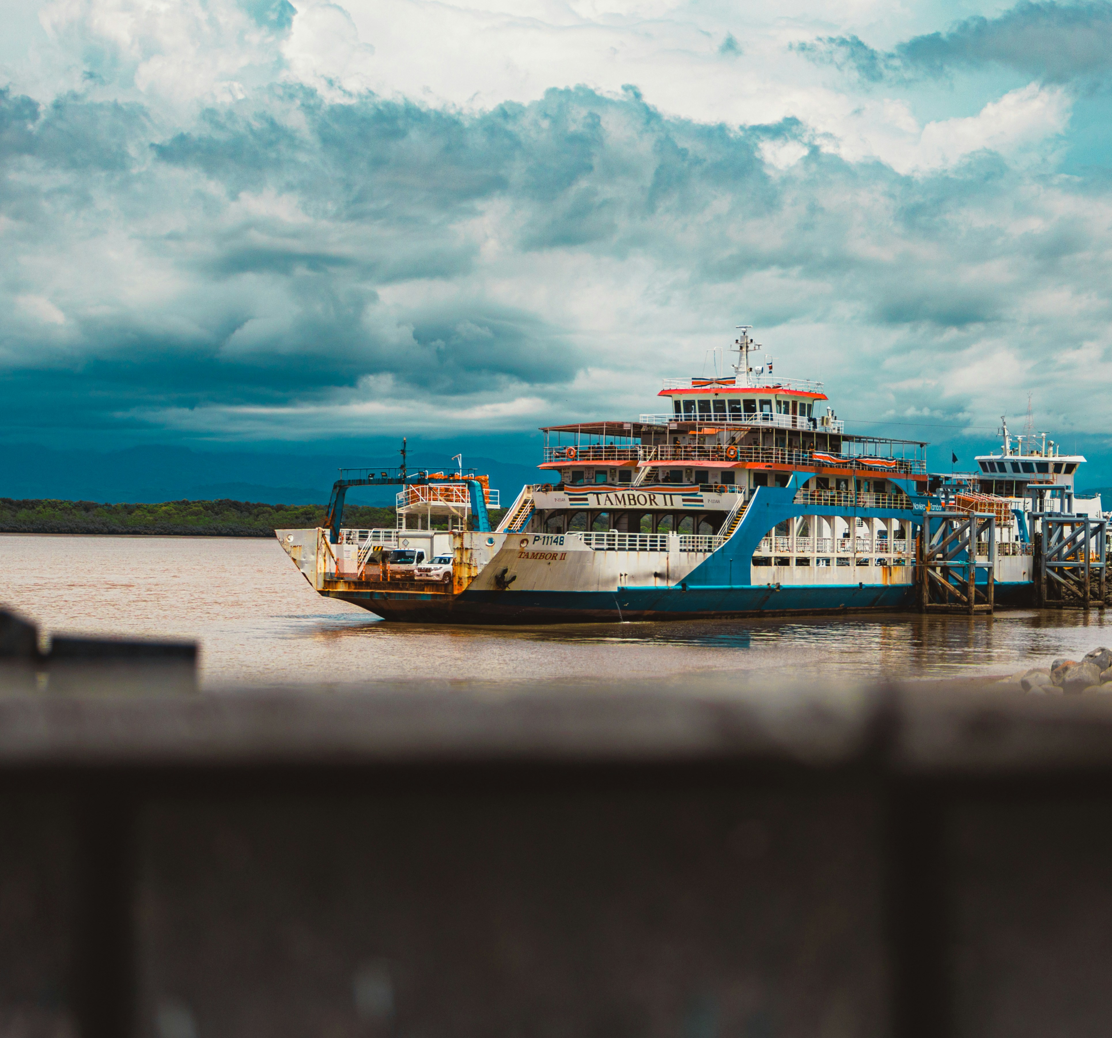 Docked Journey: Blue and White Ferry Nestled by Stormy Skies