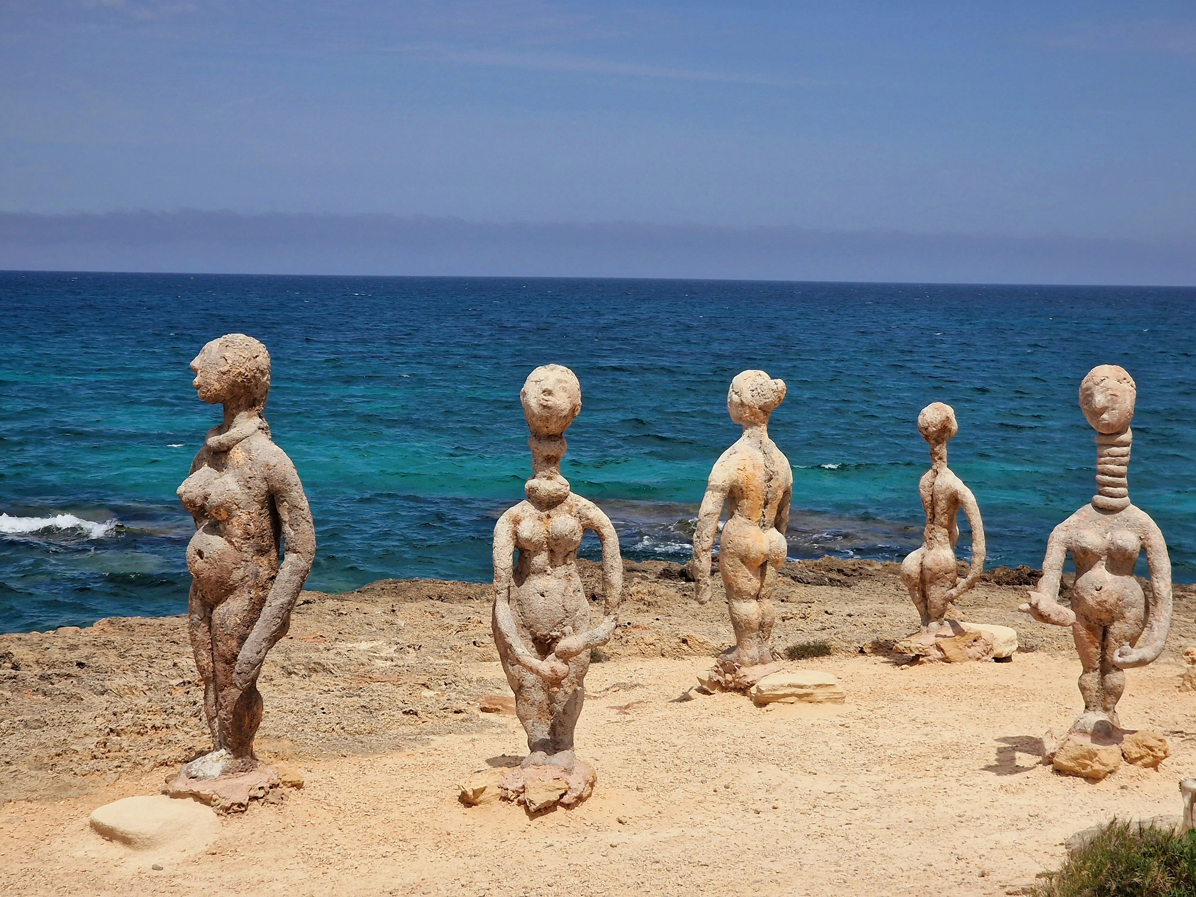 Grouped stone figures stand vigil along sunlit shoreline
