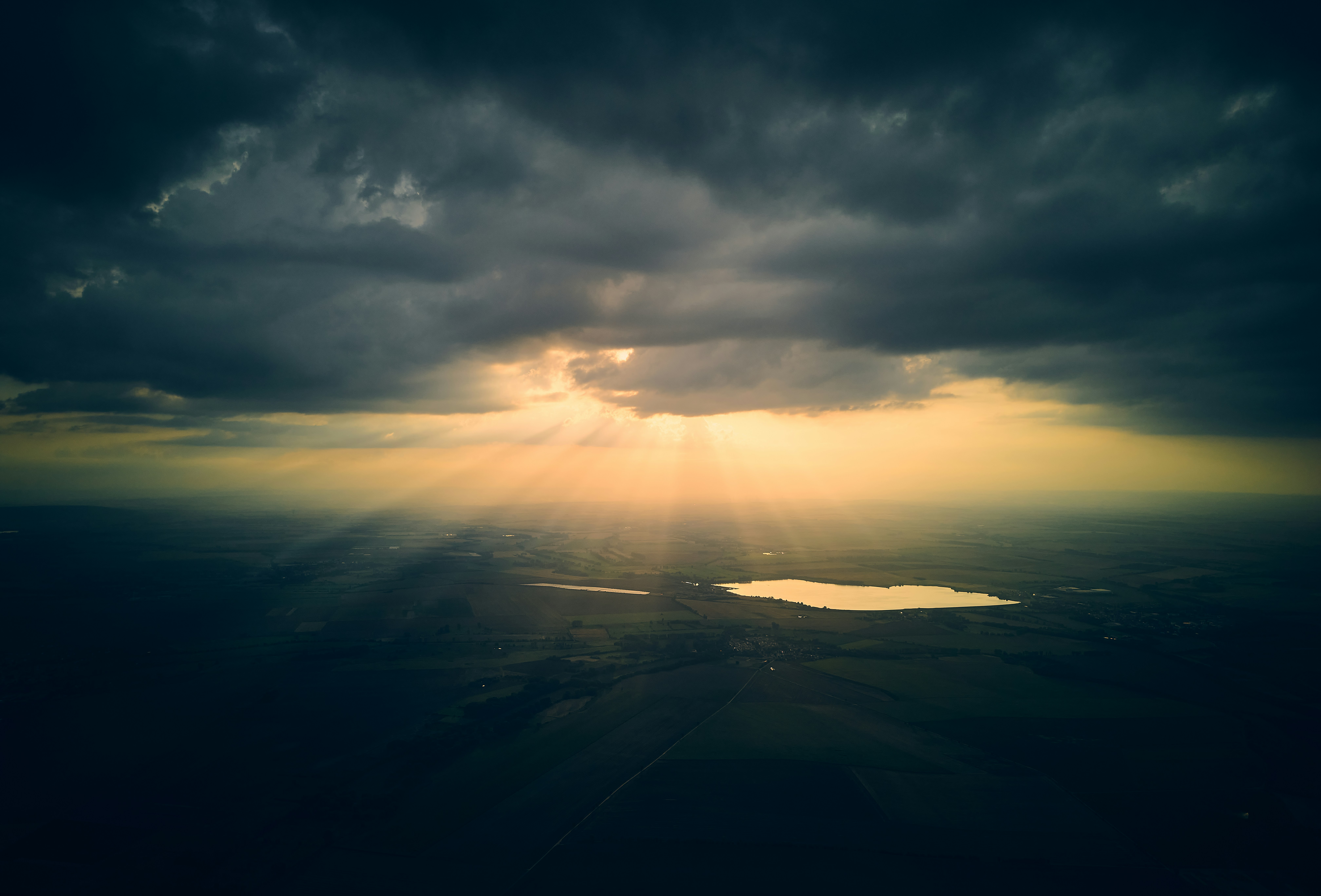 Sunbeams break through dark storm clouds over landscape.