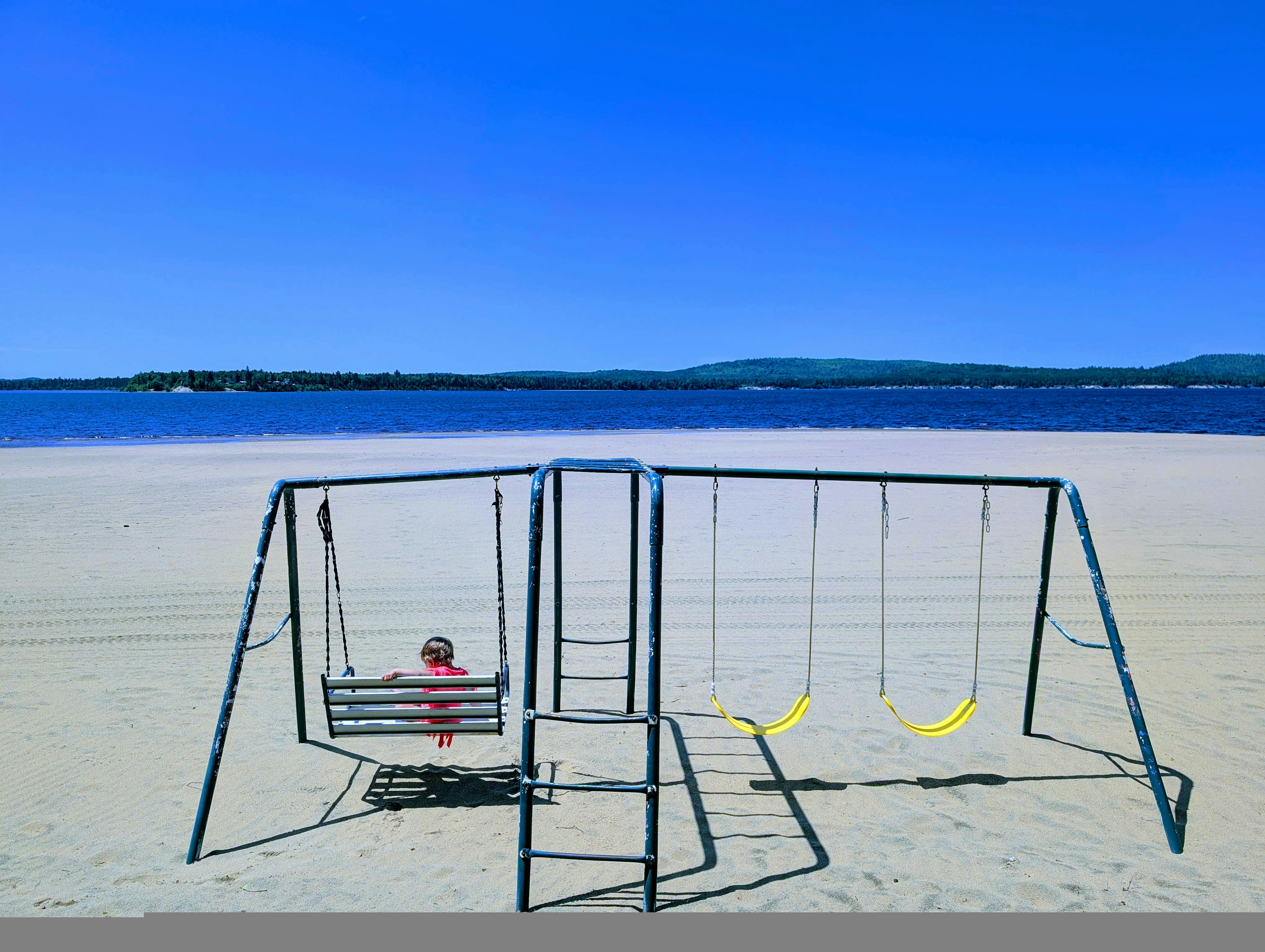 Child on a Swing Set Framed by a Pristine Beach and Blue Sky