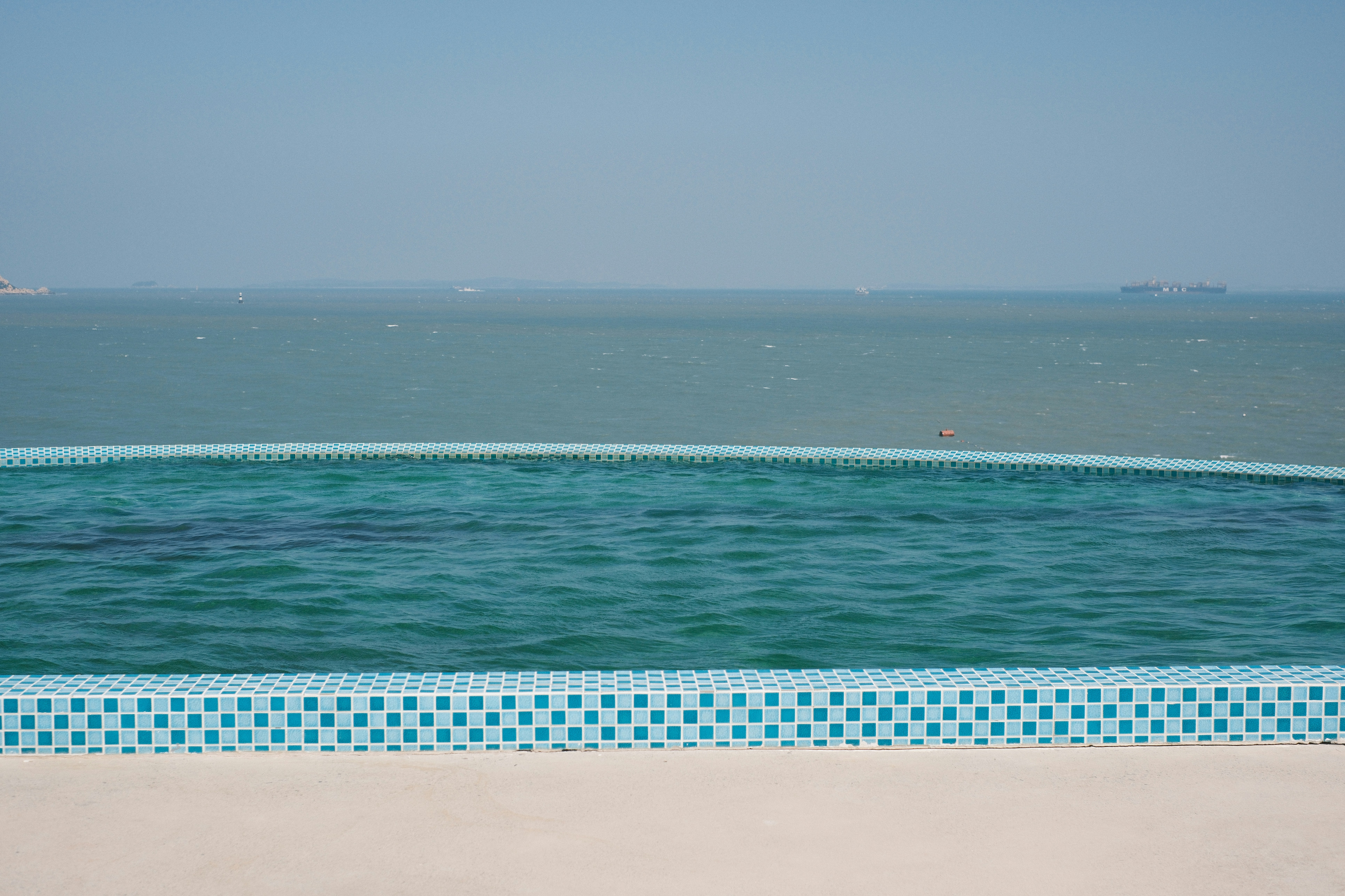 Poolside Horizon: Blue Tile Barrier and Calm Sea