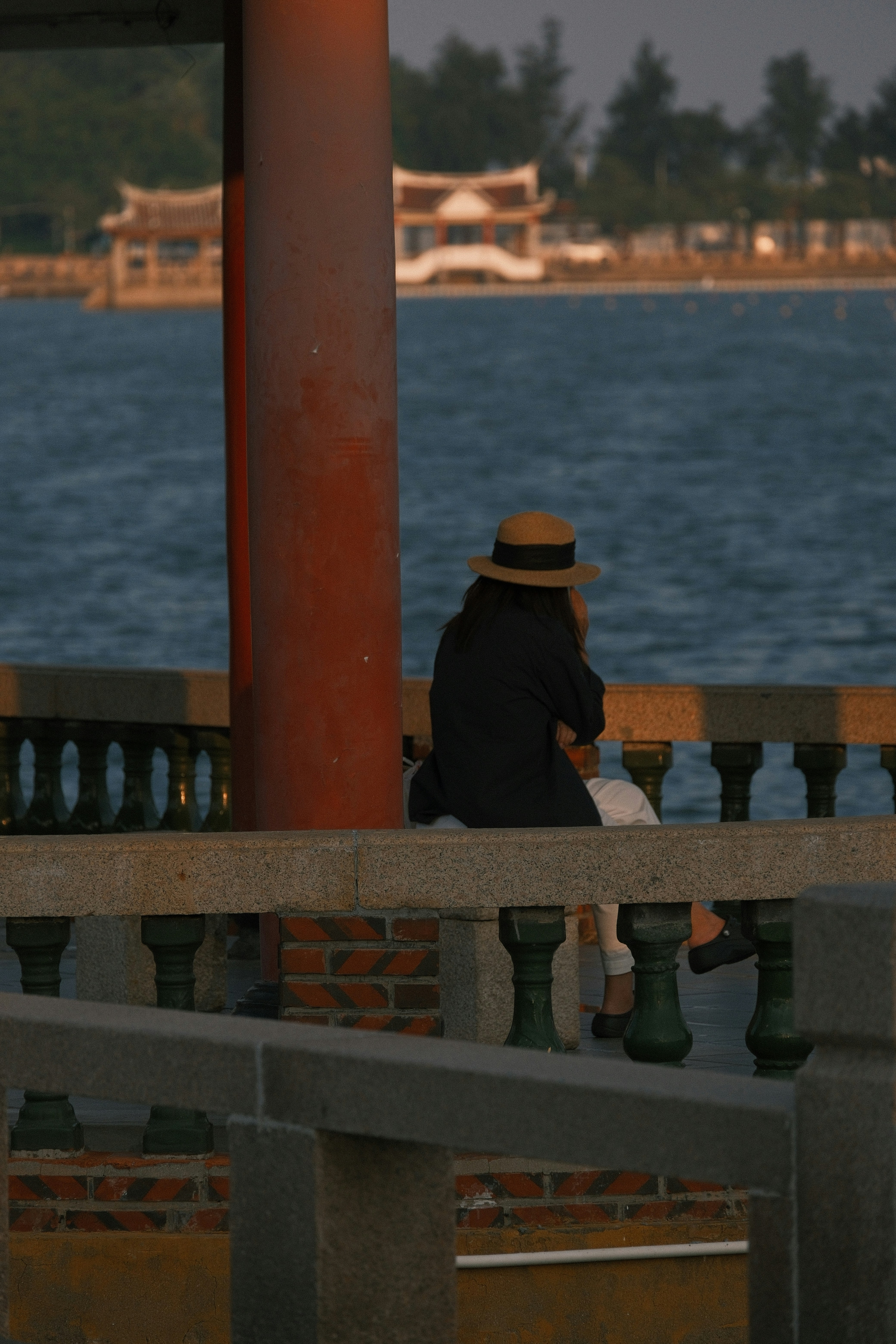 Quiet Harbor: A woman in a straw hat gazes toward the water from a seaside promenade