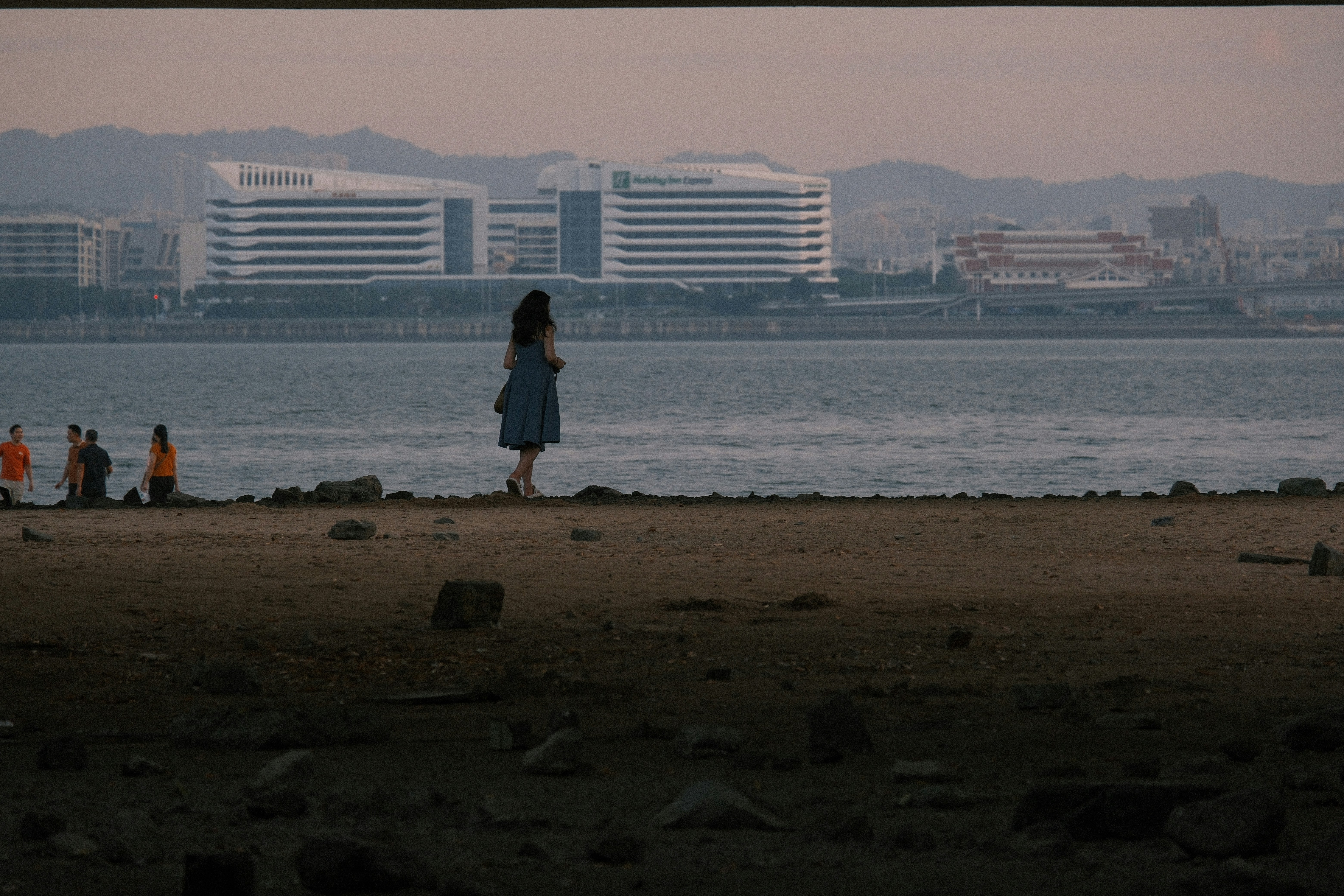 Solitary figure by the shoreline as cityscape glows in the distance