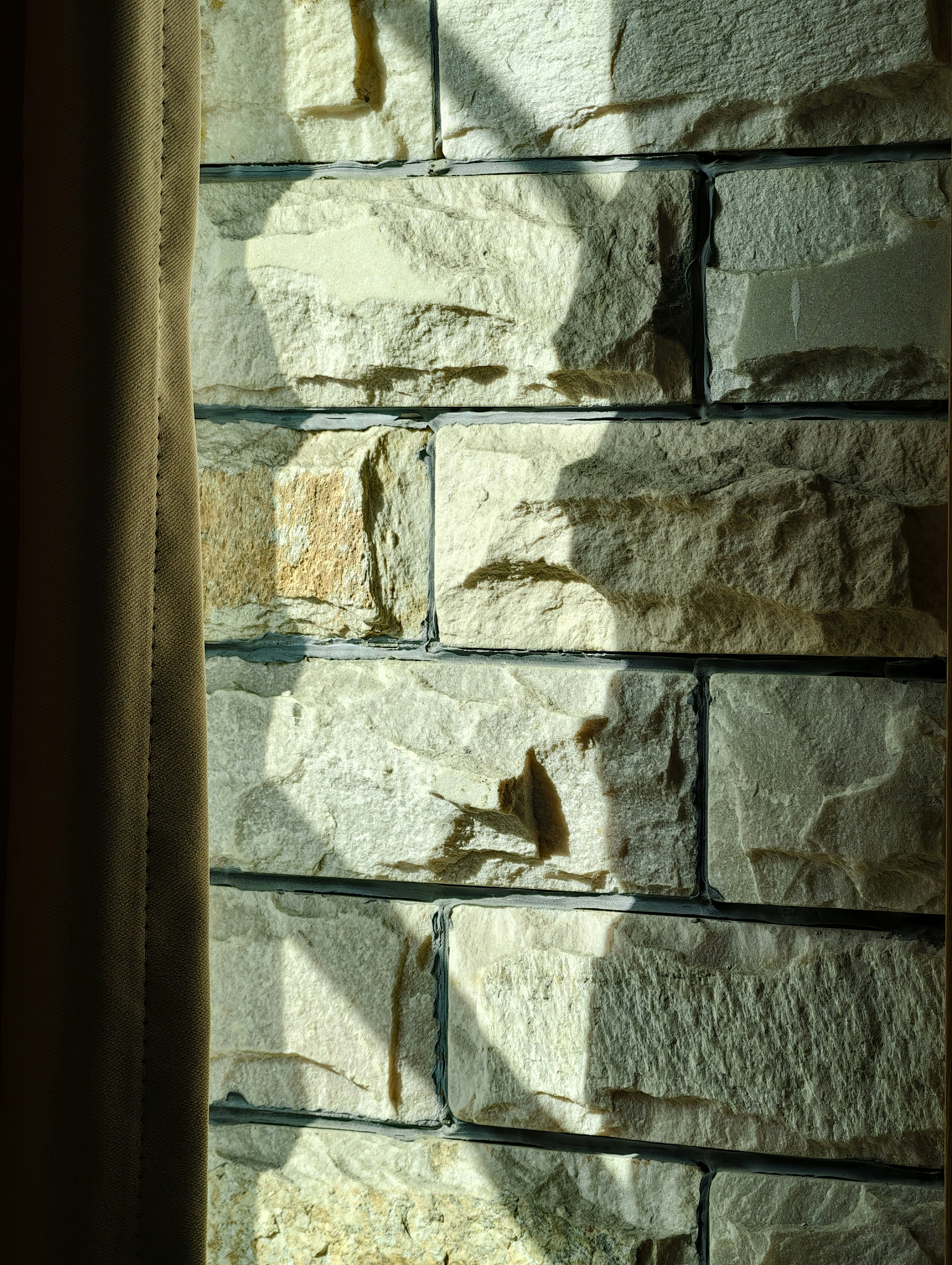Sunlight shines on a stone wall next to curtain.