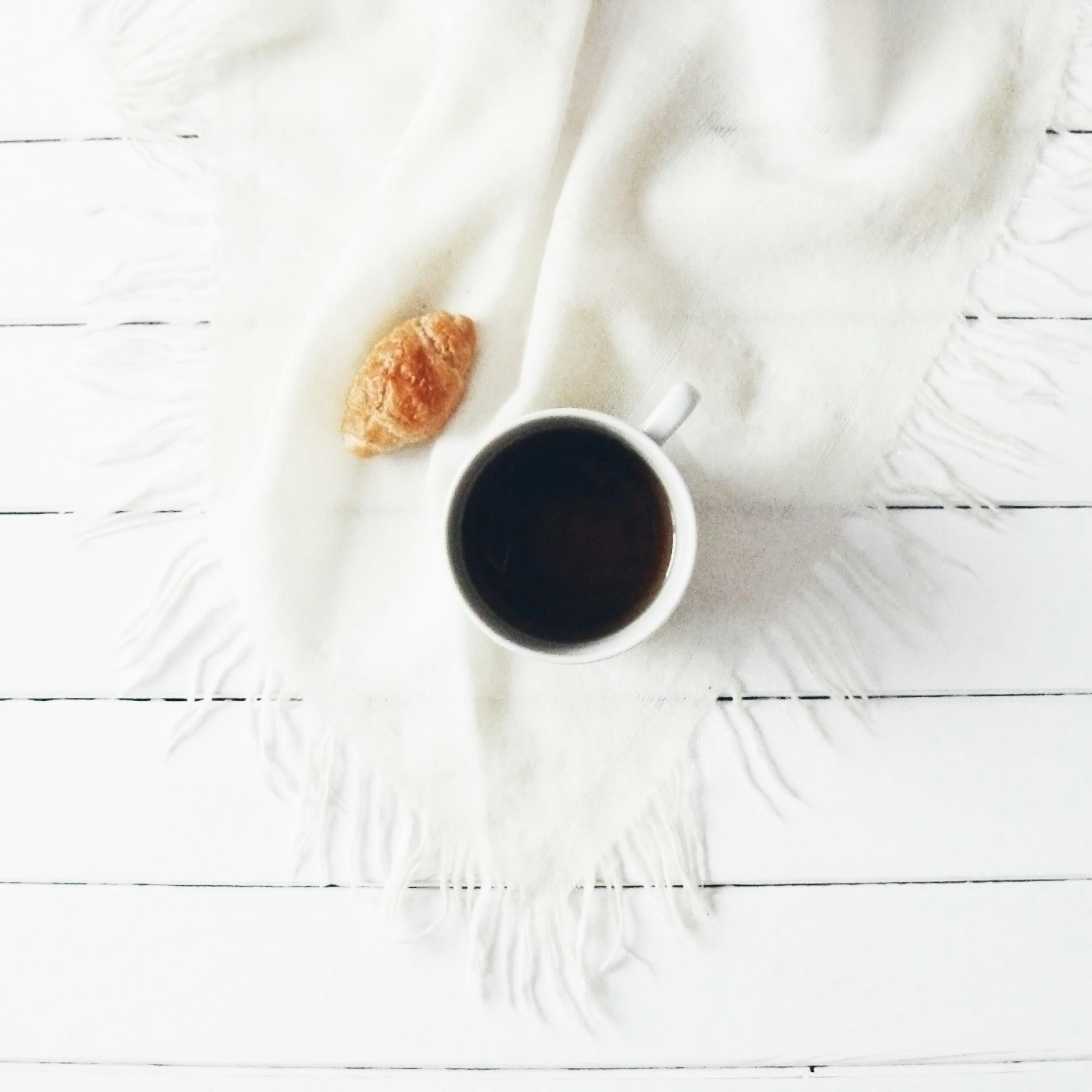 Quiet Morning: A Cup of Coffee and a Croissant on White Planks