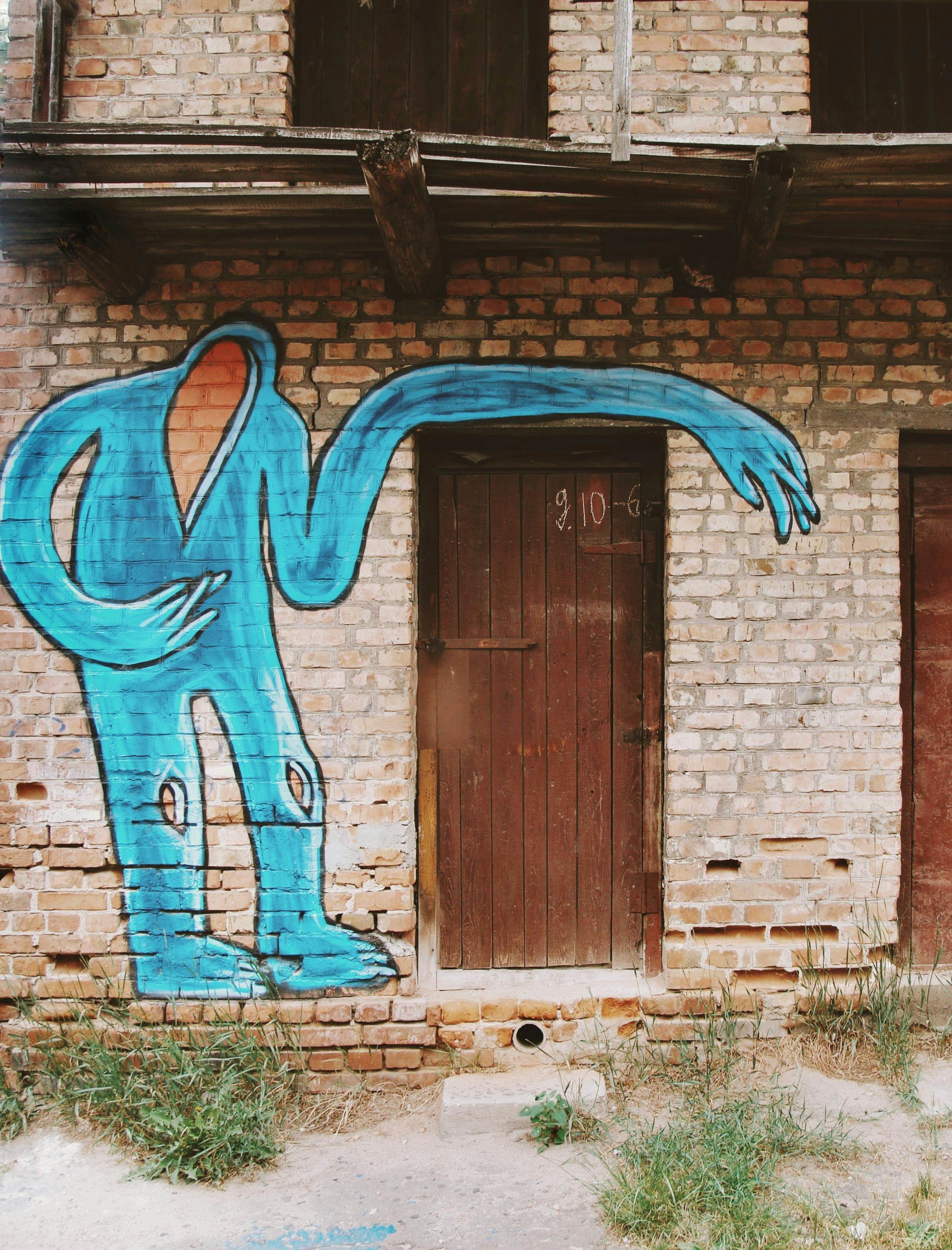 Blue Reclining Arm: Graffiti Character Anchoring a Weathered Brick Doorway