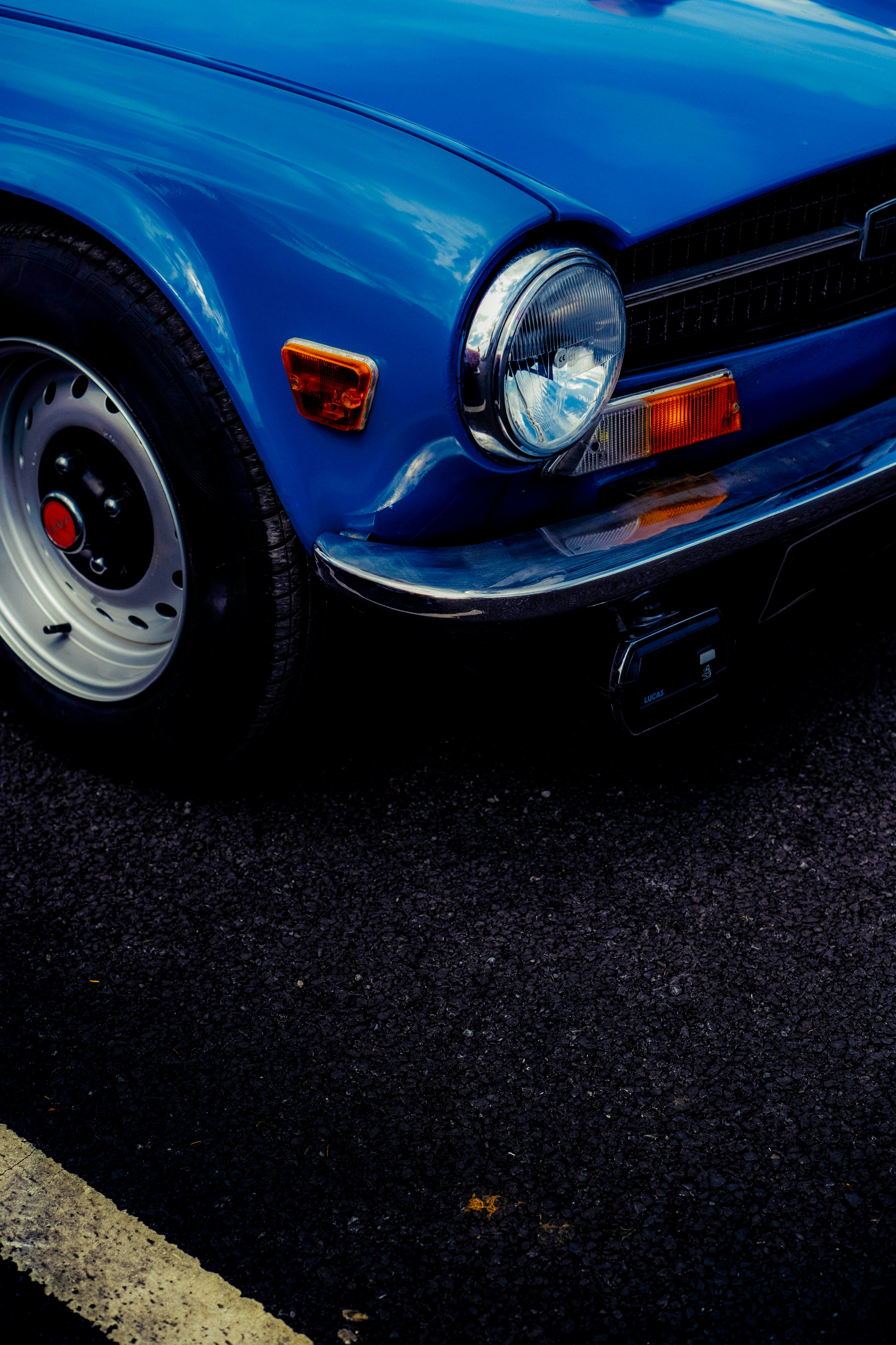 Blue classic car headlight with chrome bumper and wheel in focus