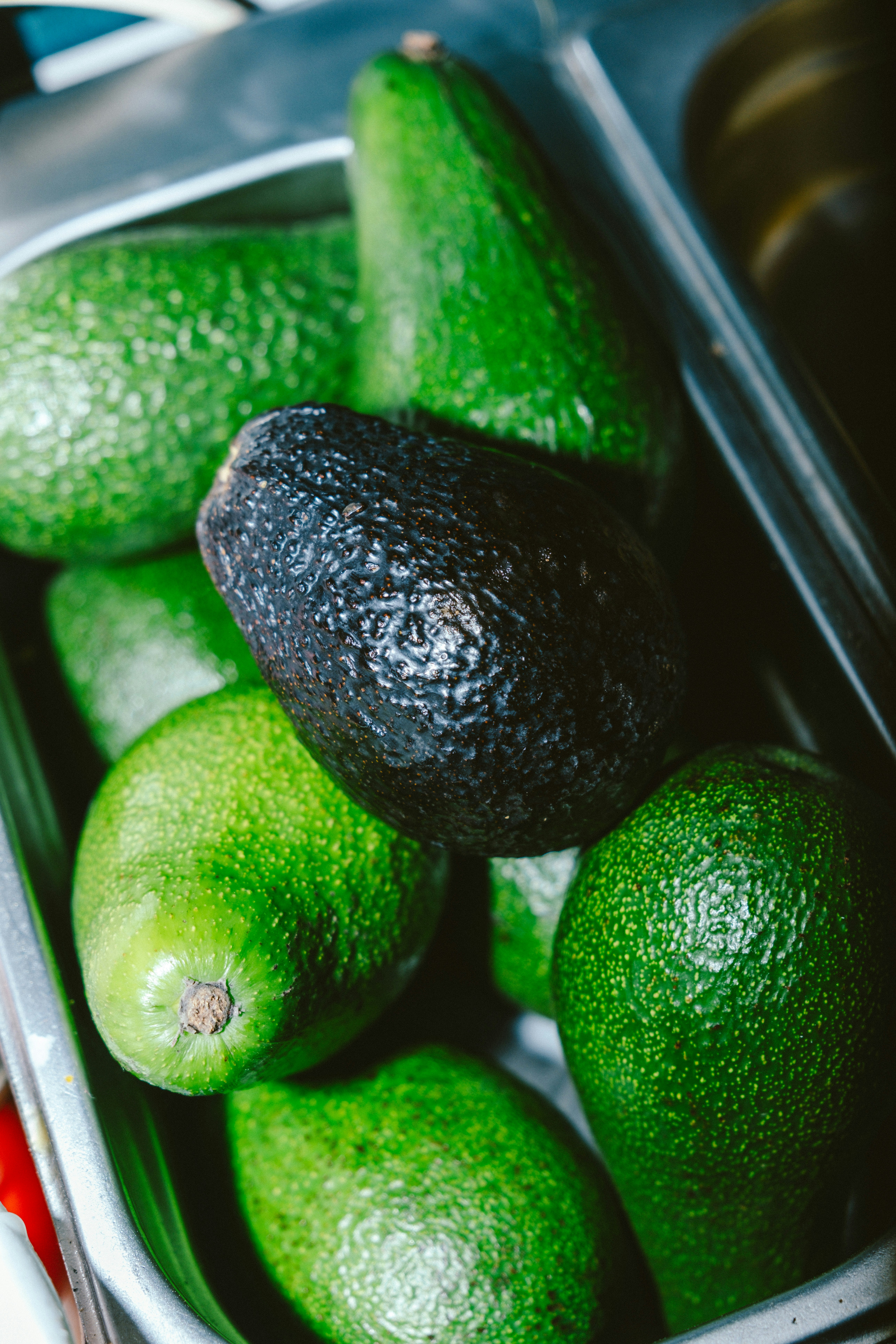 A pile of ripe avocados in a metal container.