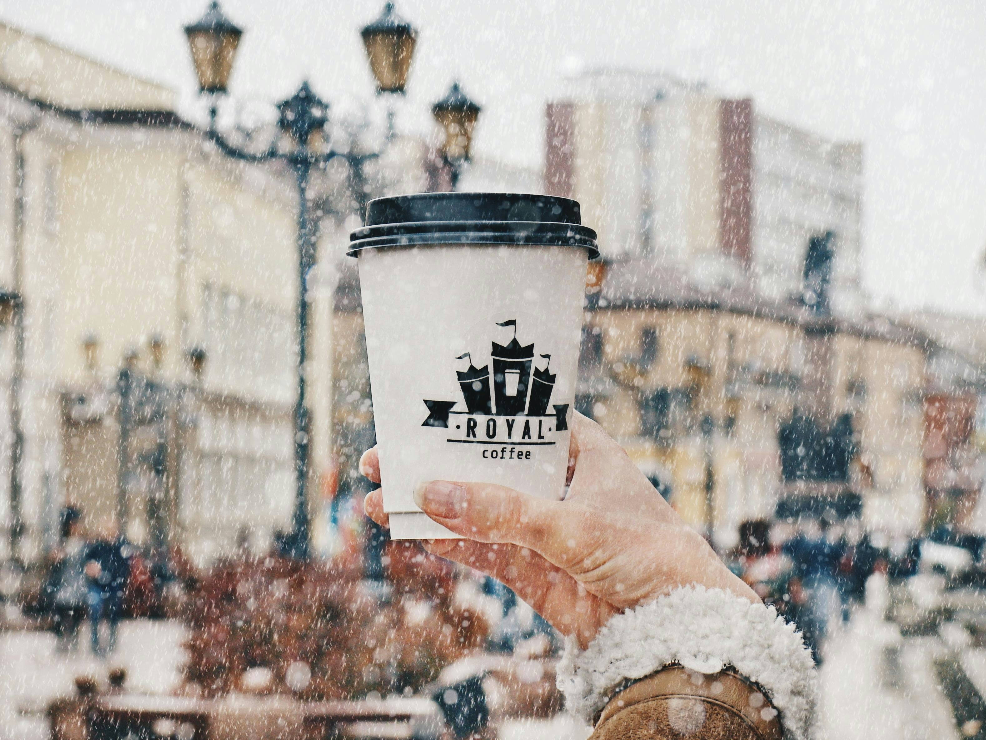 Holding Warmth: A Snowy Street Moment with a Coffee Crown
