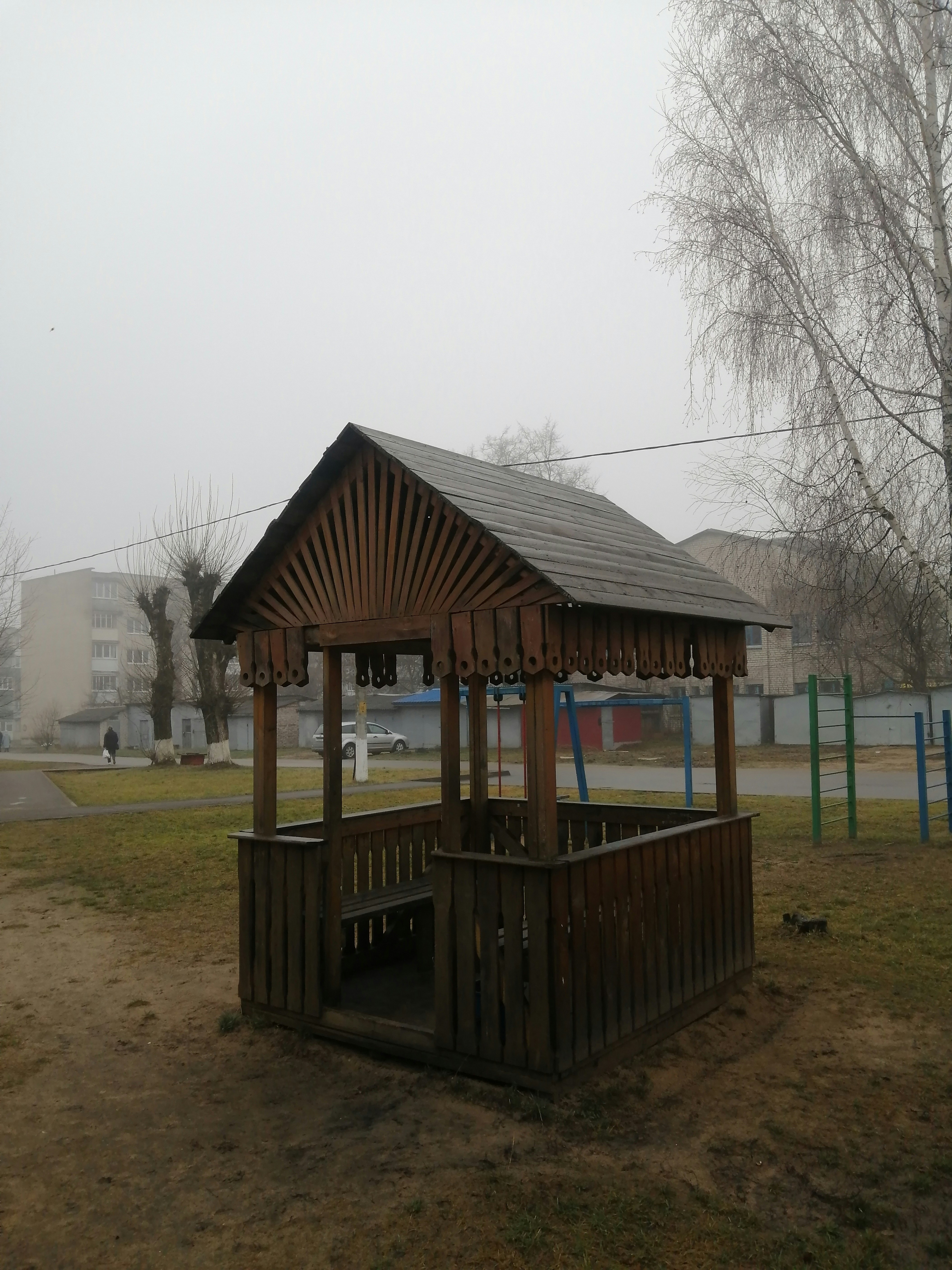 Wooden gazebo in a foggy park under bare trees