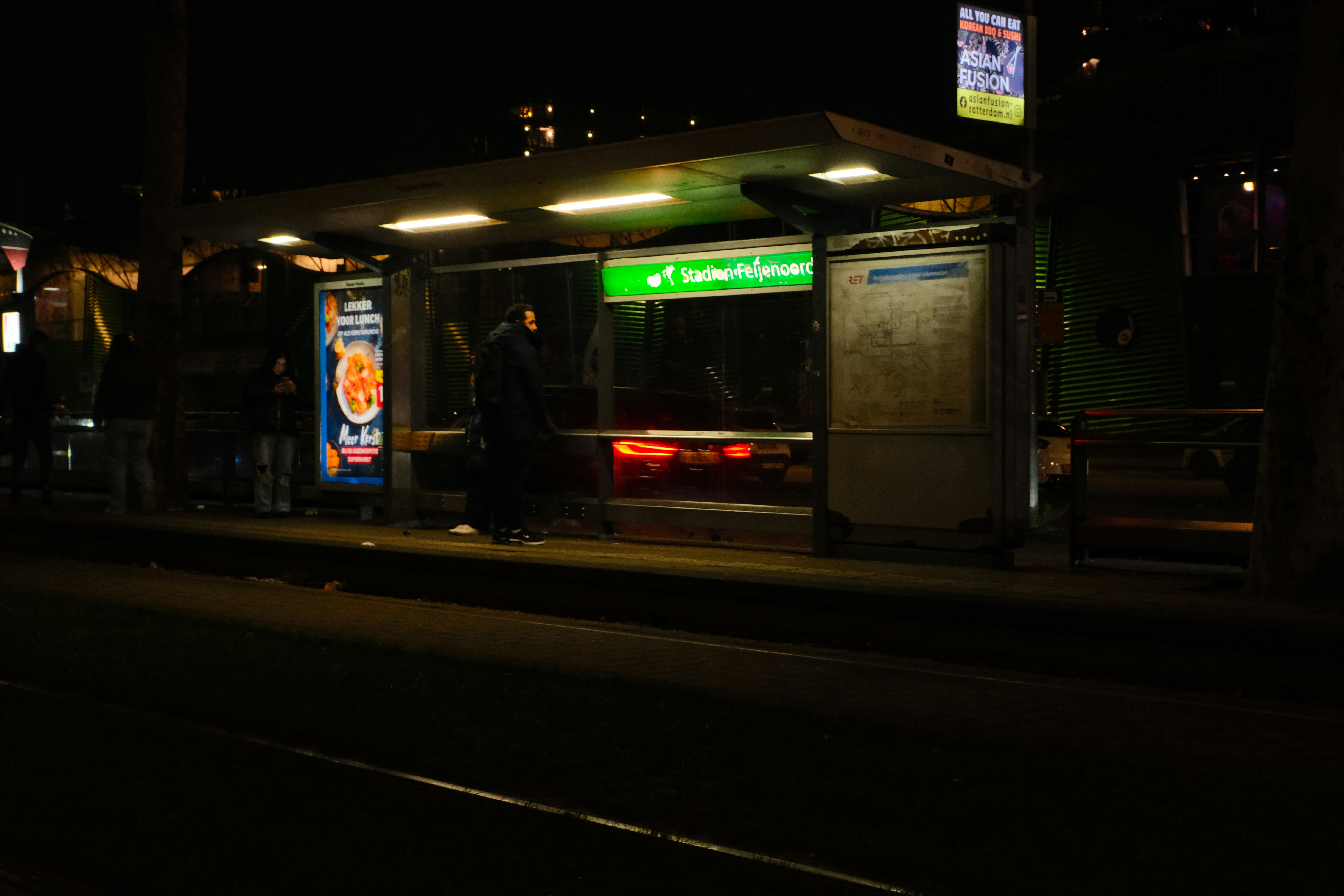 A person waits at a bus stop at night.