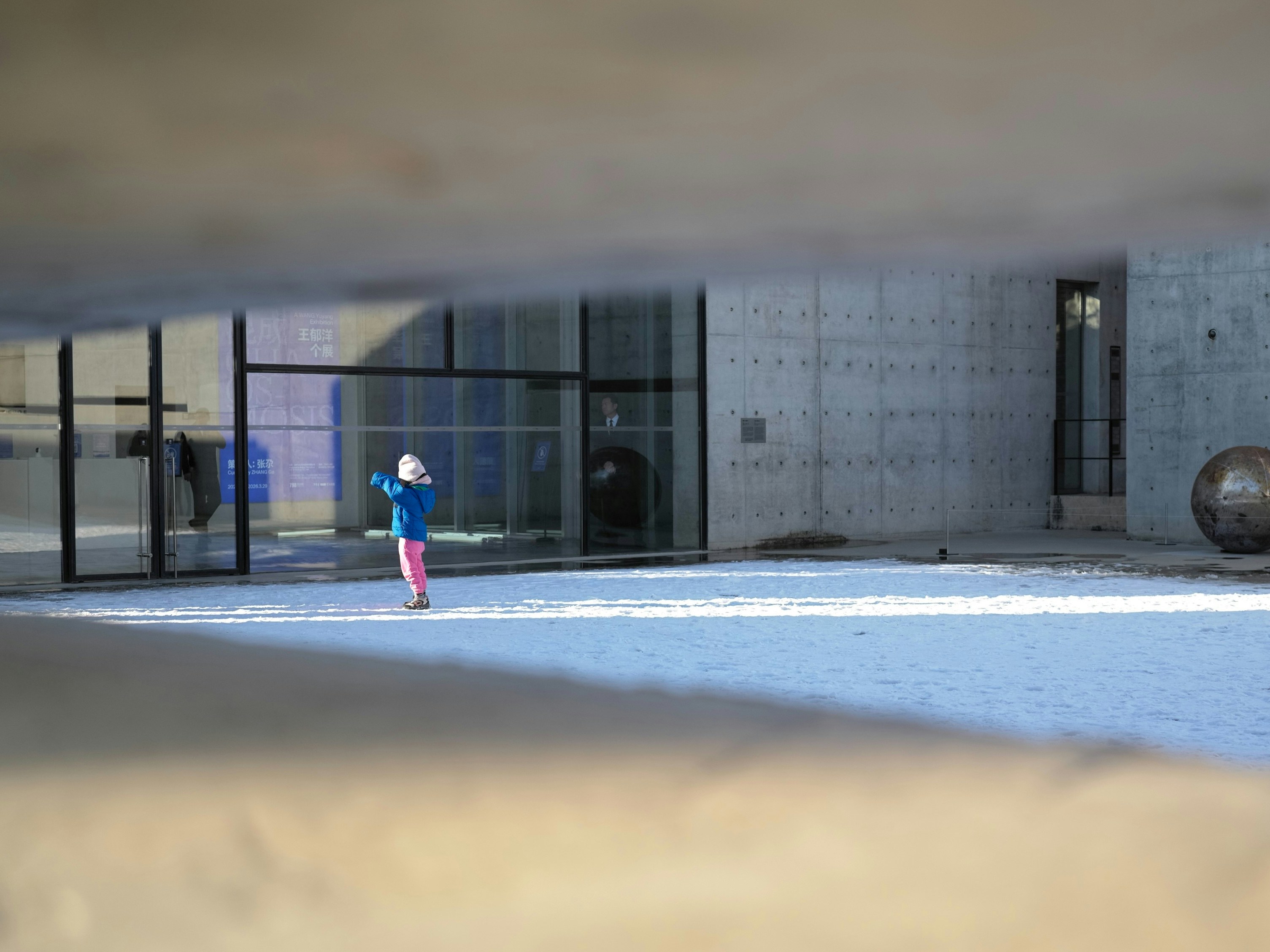 Child in blue jacket stands near modern building
