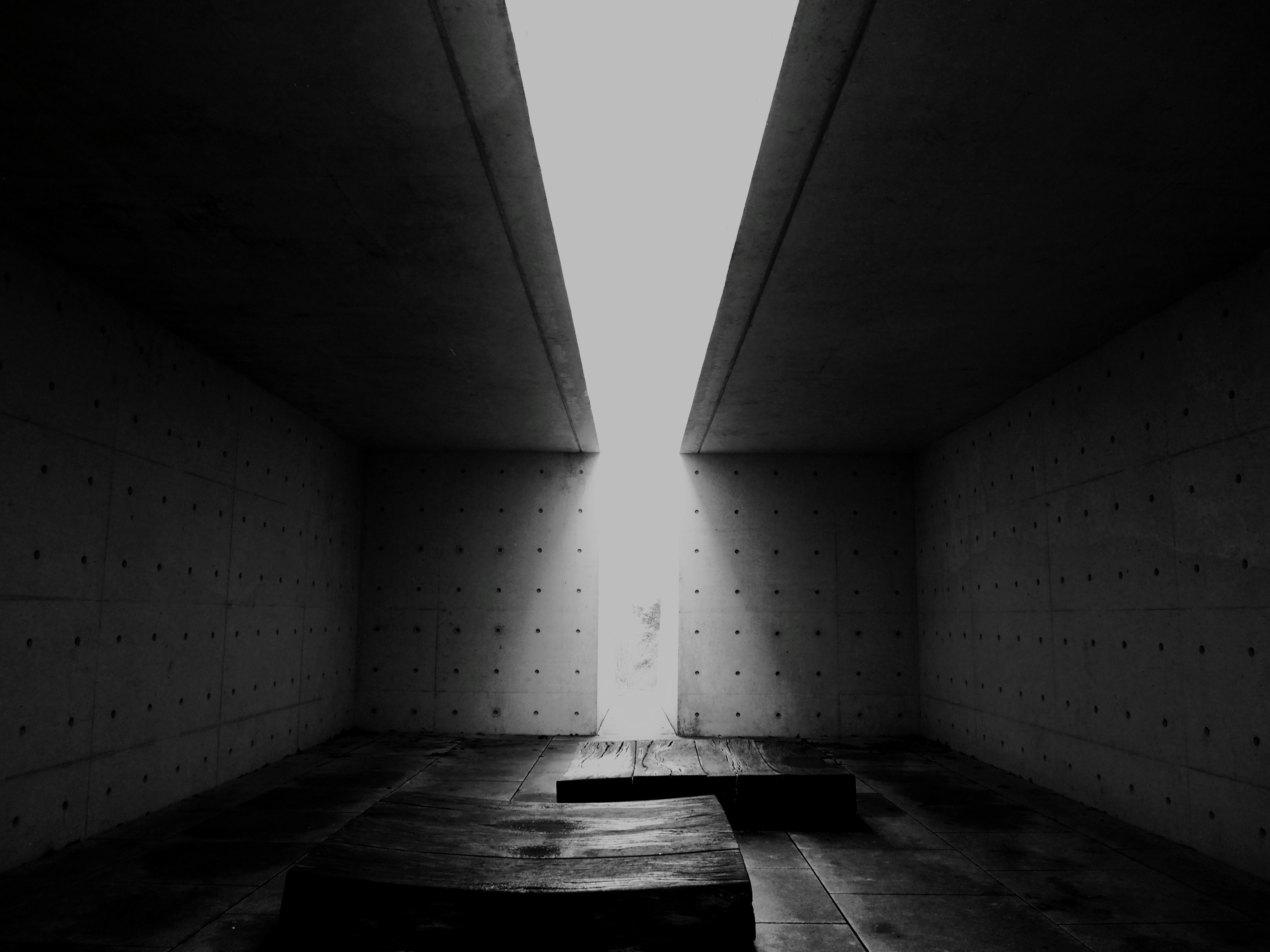 Interior view of the Tulach a’ tSolais monument in County Wexford, Ireland, commemorating the 1798 Rebellion. The concrete chamber is split by a narrow vertical opening that draws daylight into the dark interior, creating a stark contrast between shadow and light. Designed as a place of reflection rather than spectacle, the minimalist architecture and raw materials evoke loss, resilience, and remembrance, framing the surrounding landscape through a controlled shaft of sky.