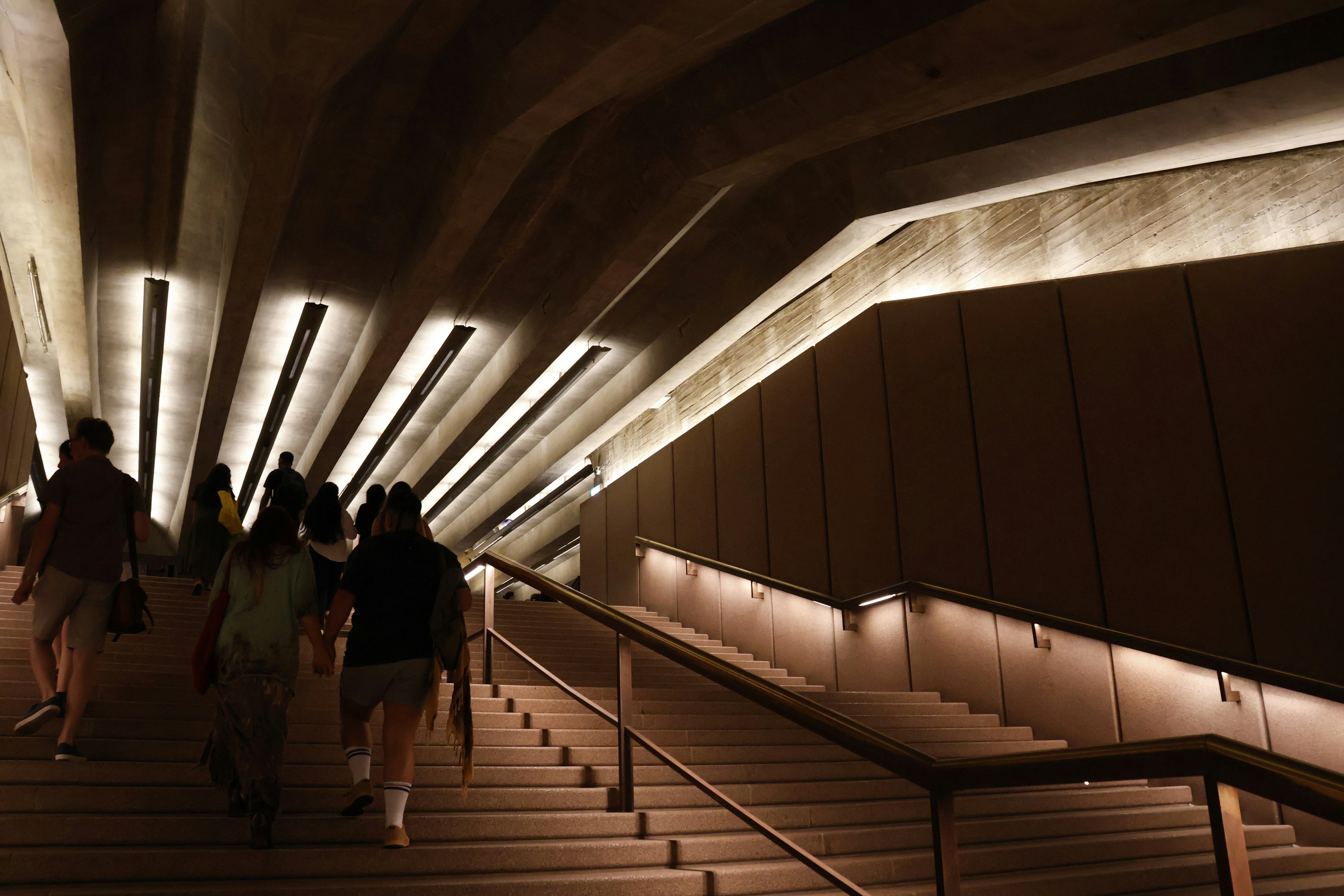 Shadowed Ascent: Travelers in a Neon-lit Staircase Hall
