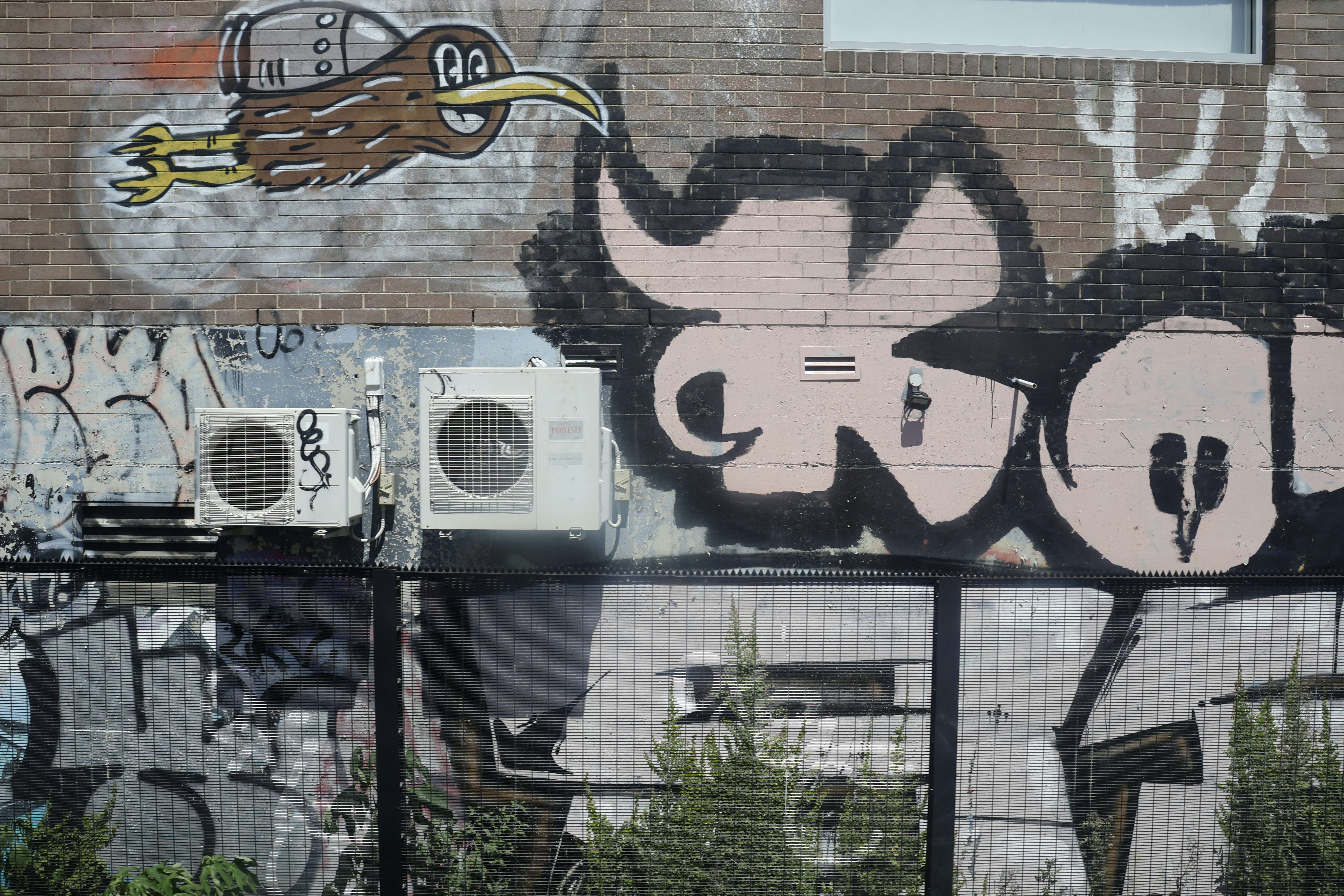 Graffiti art on a brick wall with air conditioners.