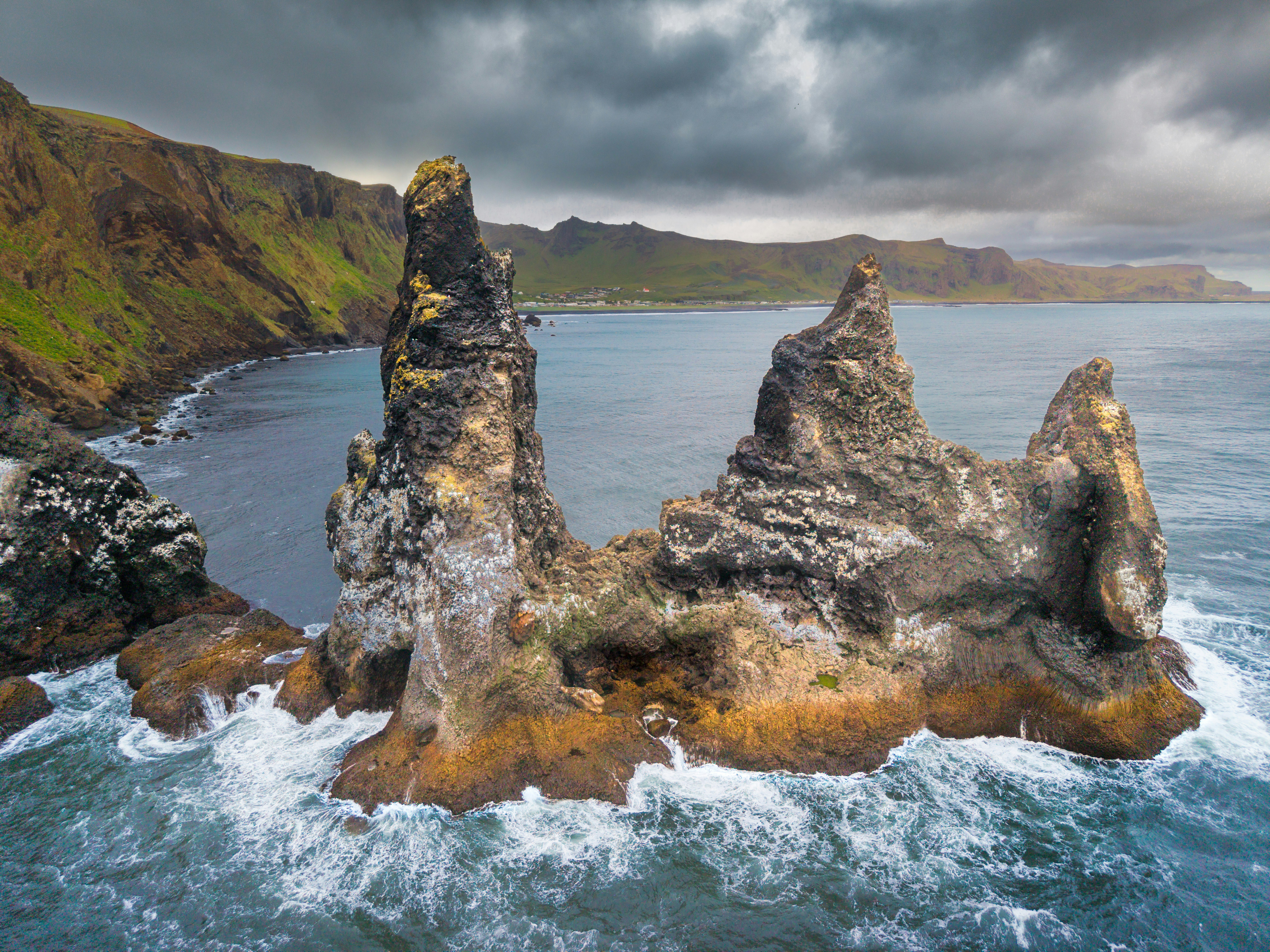 Storm clouds over the jagged sea stacks of Reynisfjall, with North Atlantic surf crashing against Iceland’s dramatic coastline.