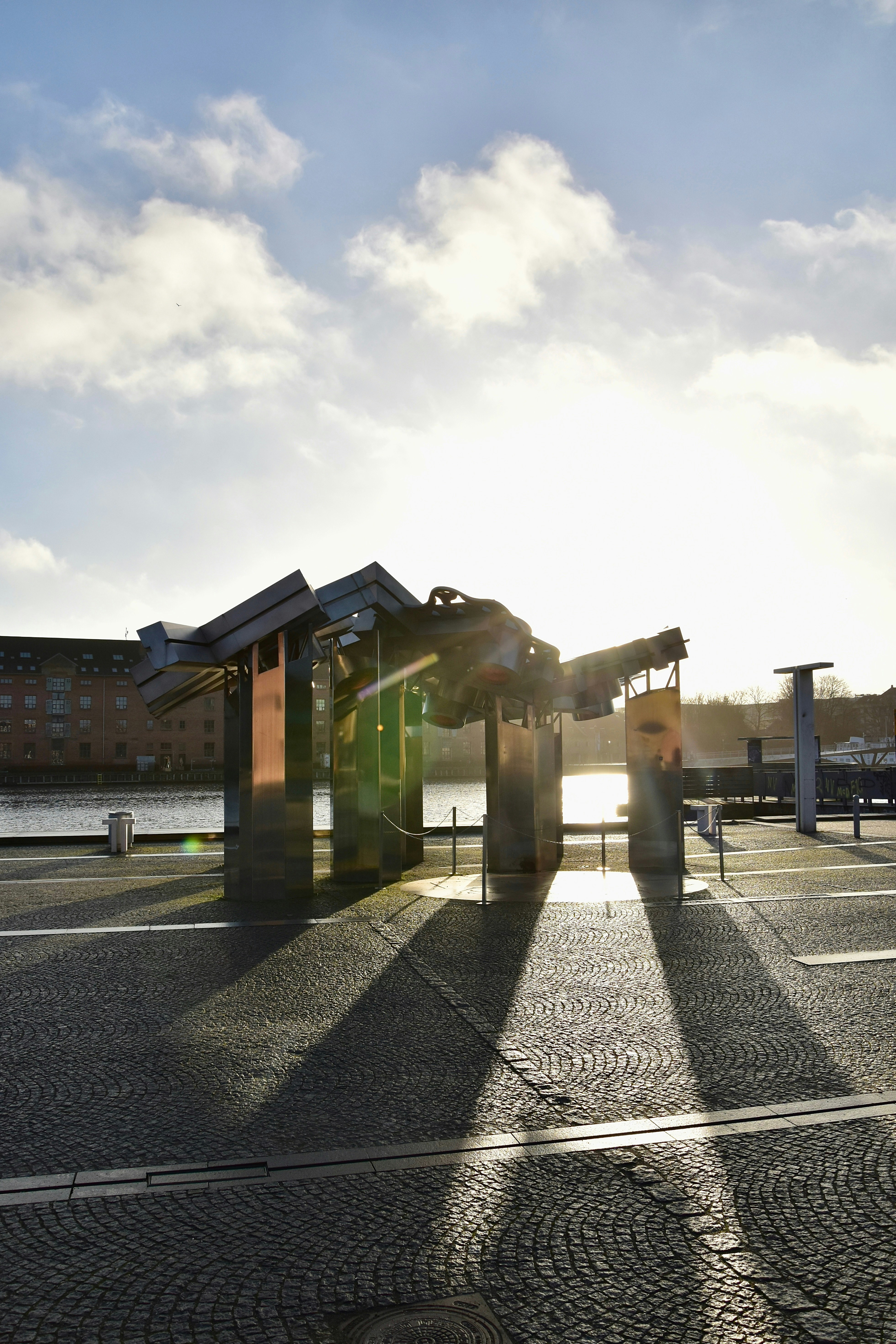 Sunlit stainless sculpture arc at the harbor edge