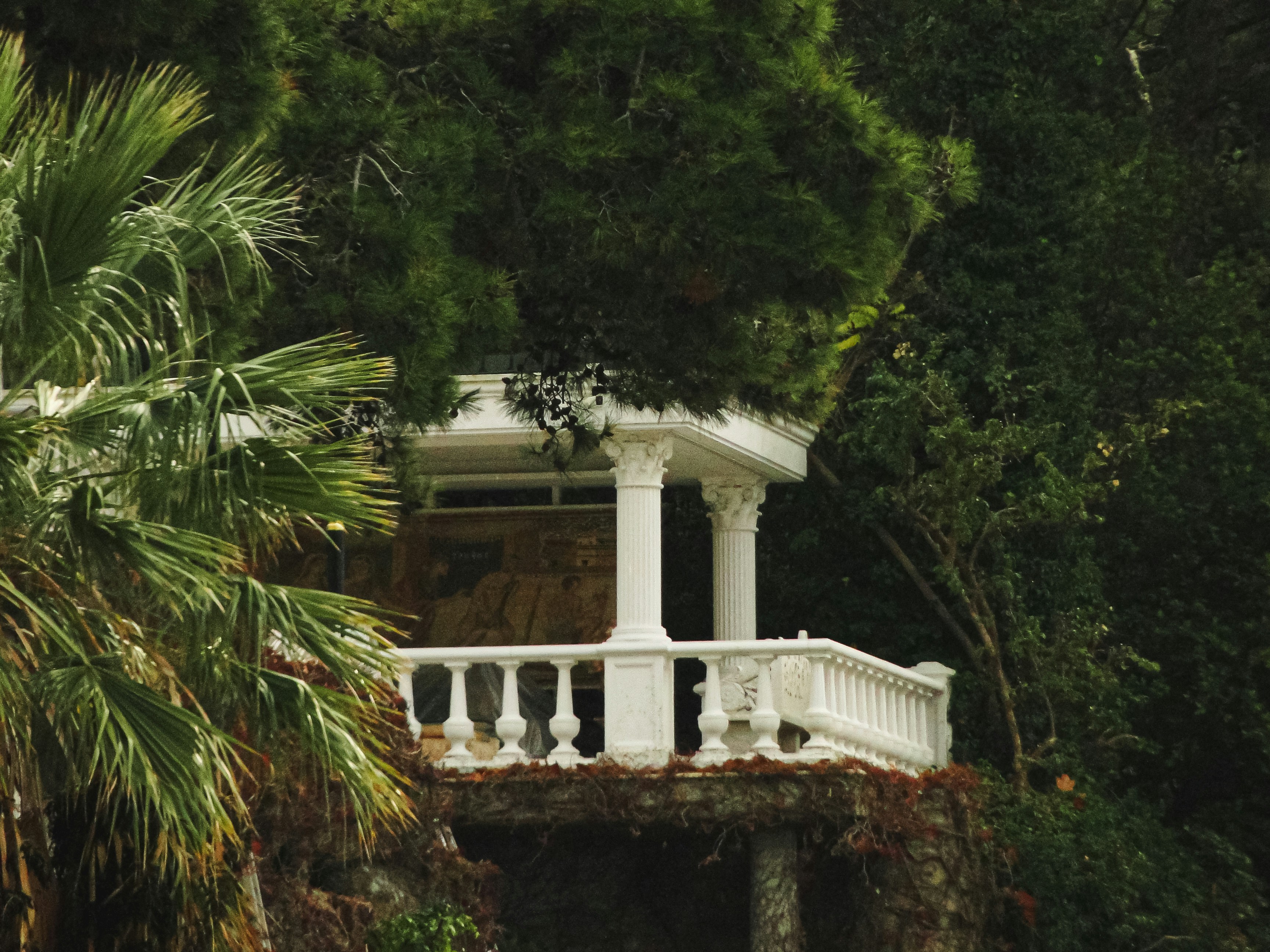 White gazebo with ornate columns amidst lush greenery