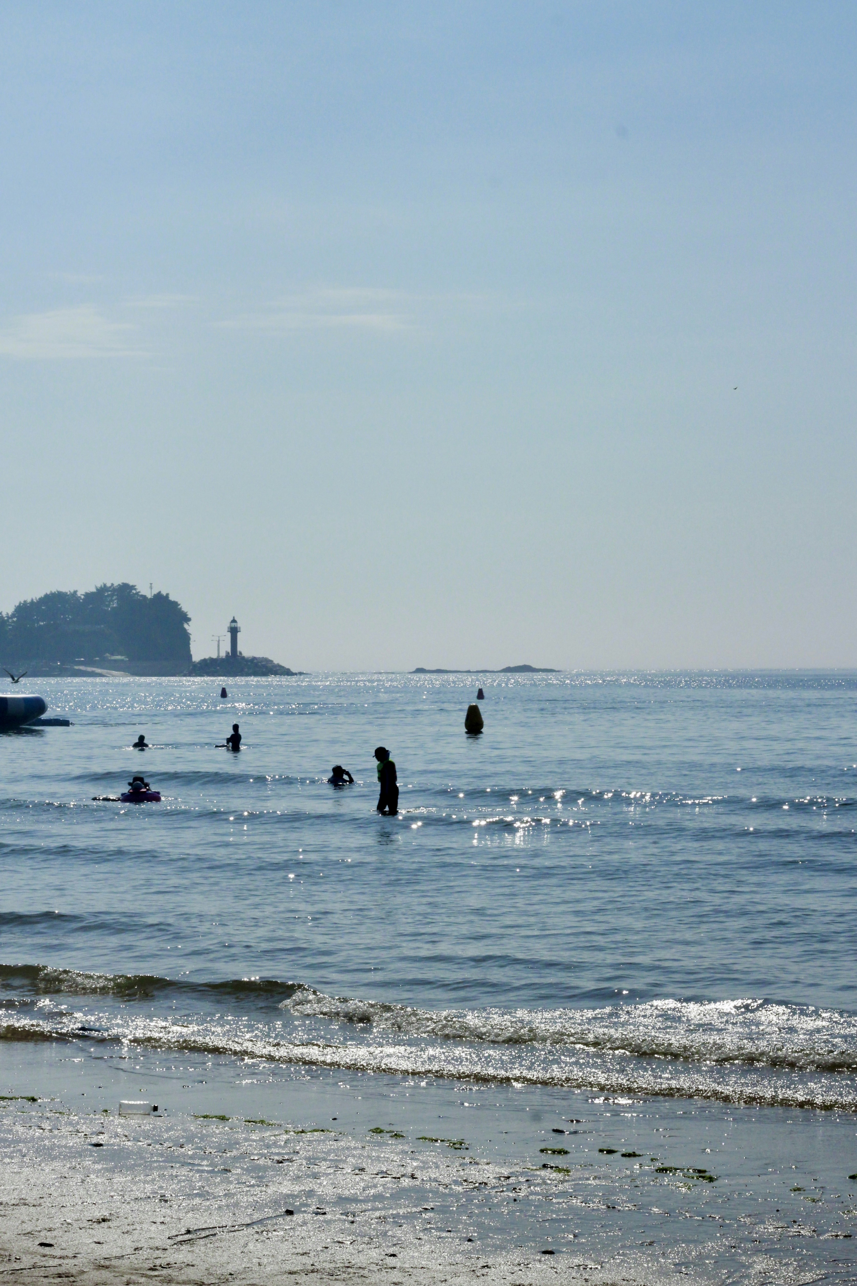People swimming in the ocean with a lighthouse in distance.