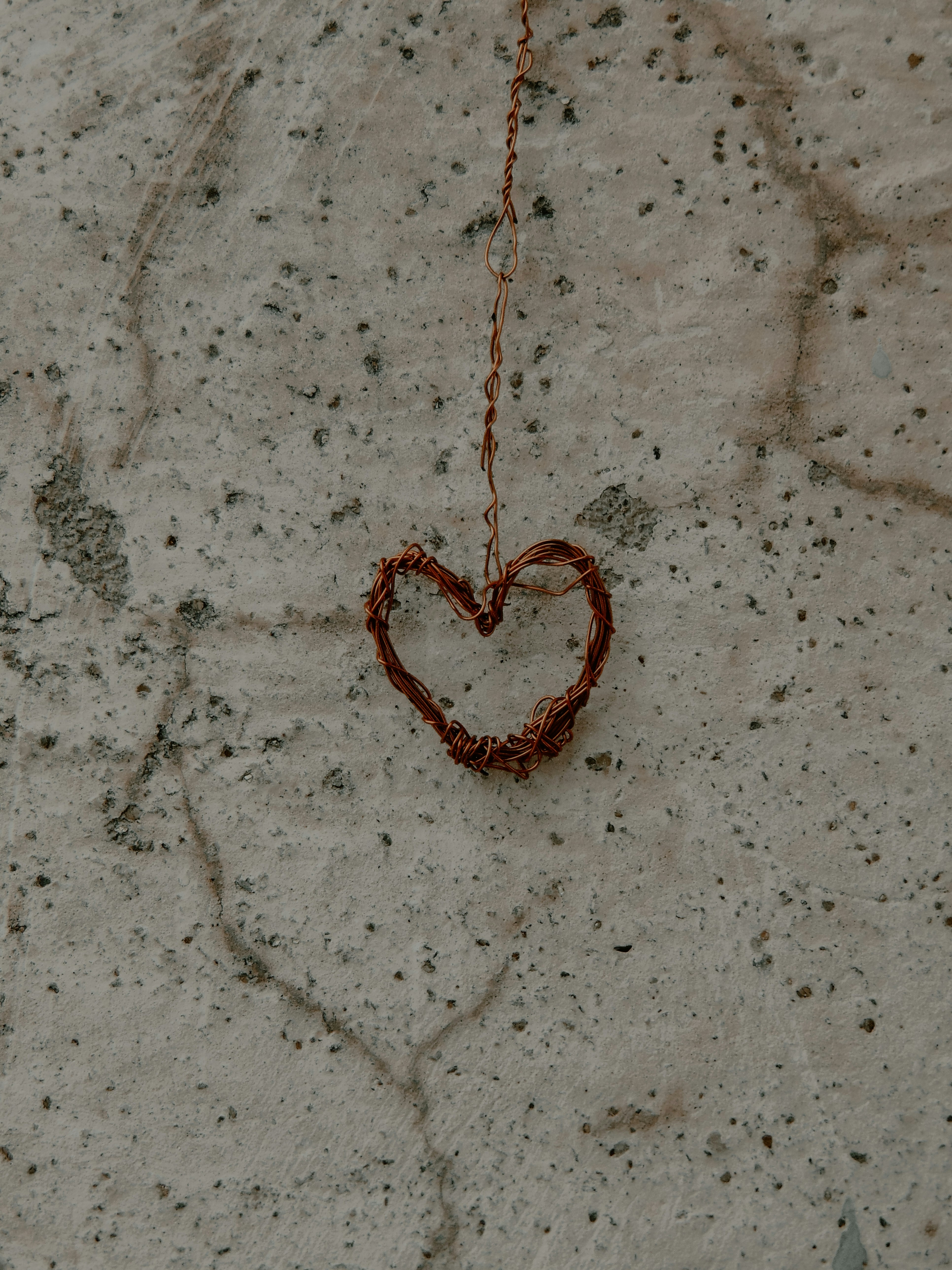 A small copper wire heart hangs against a marble background.