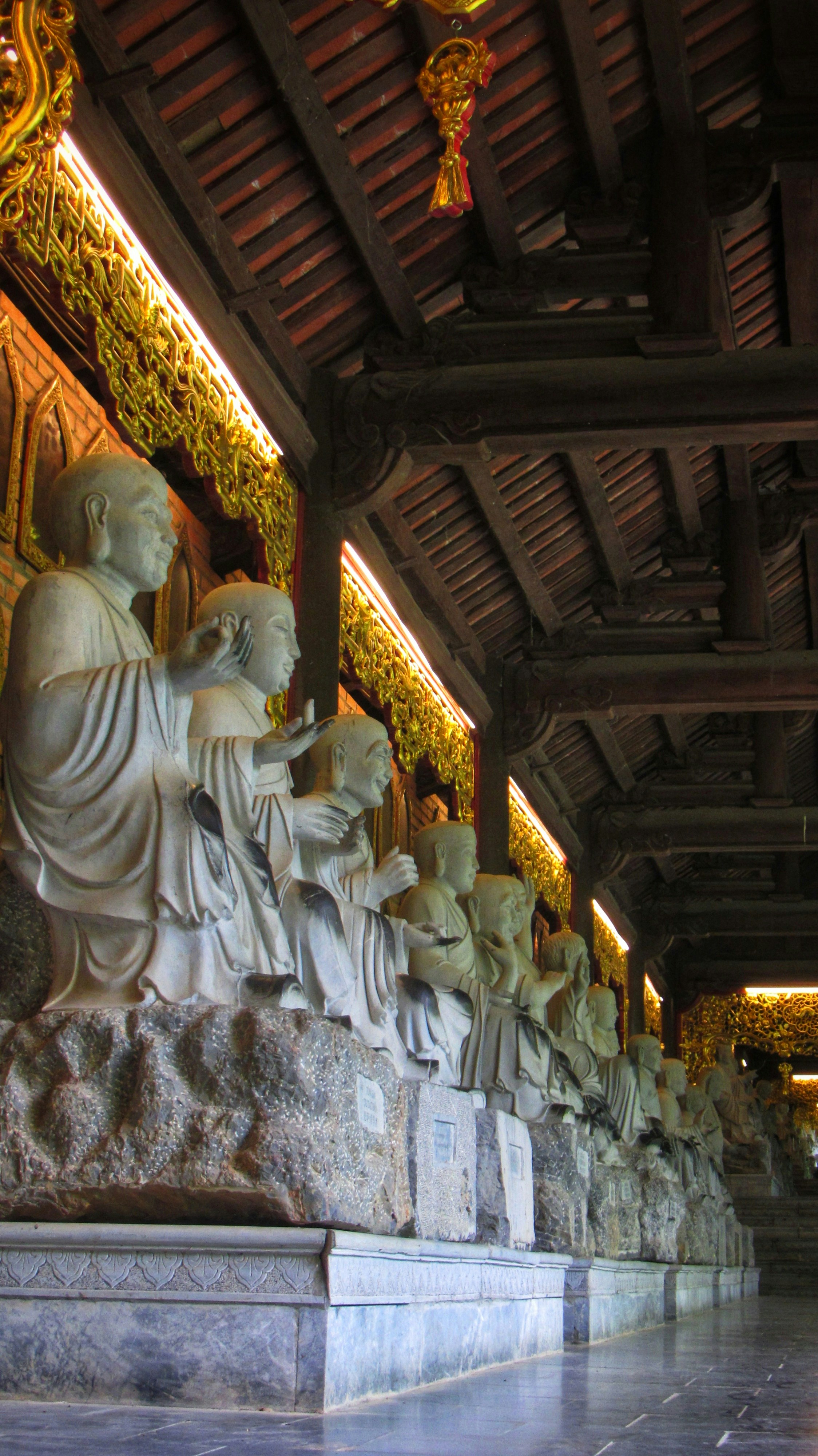 A long corridor lined with intricate stone statues of Arhats at the Bai Dinh Pagoda complex, showcasing the profound spiritual heritage and architectural beauty of Ninh Binh, Vietnam.