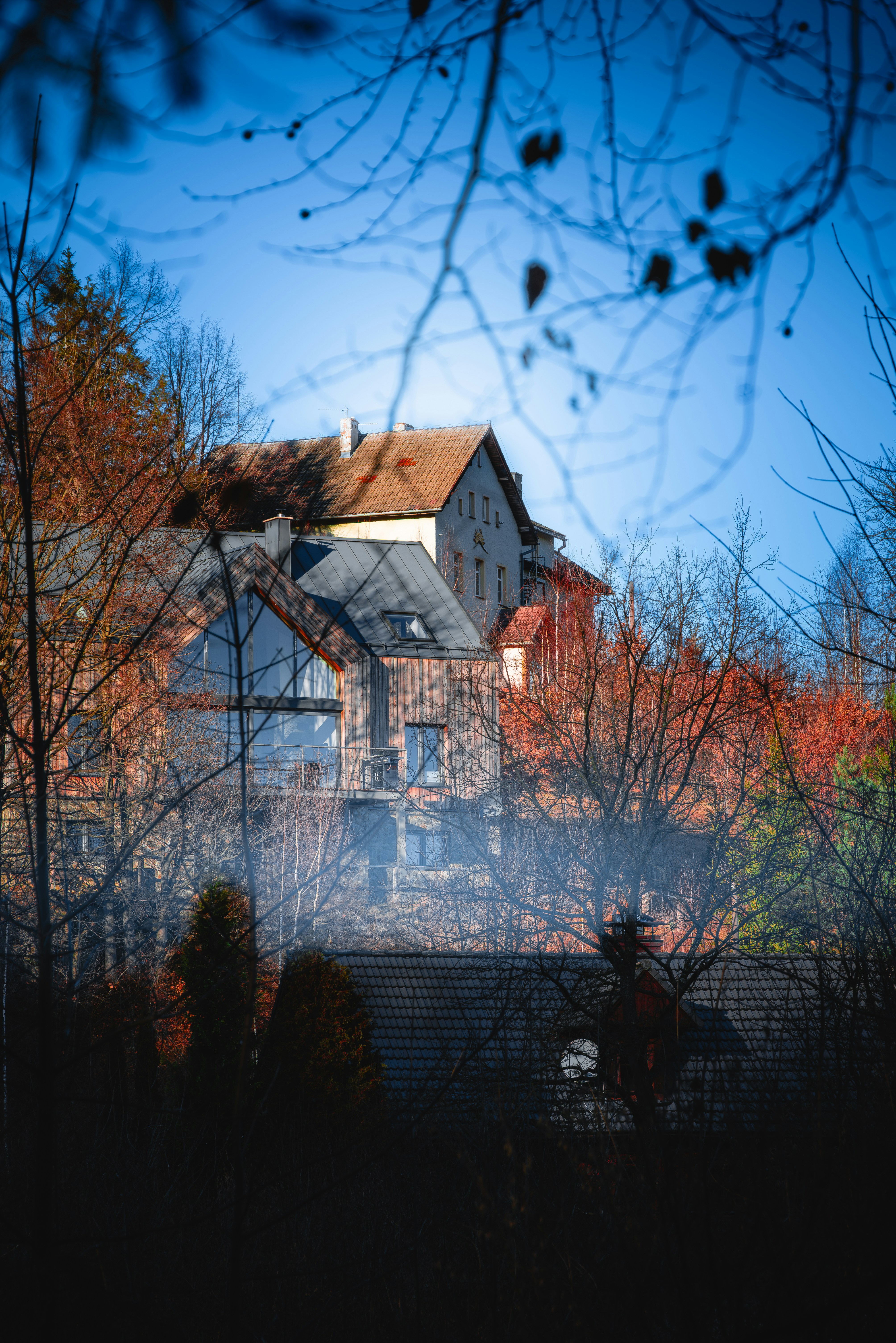 Autumn house amid blue sky, framed by bare branches
