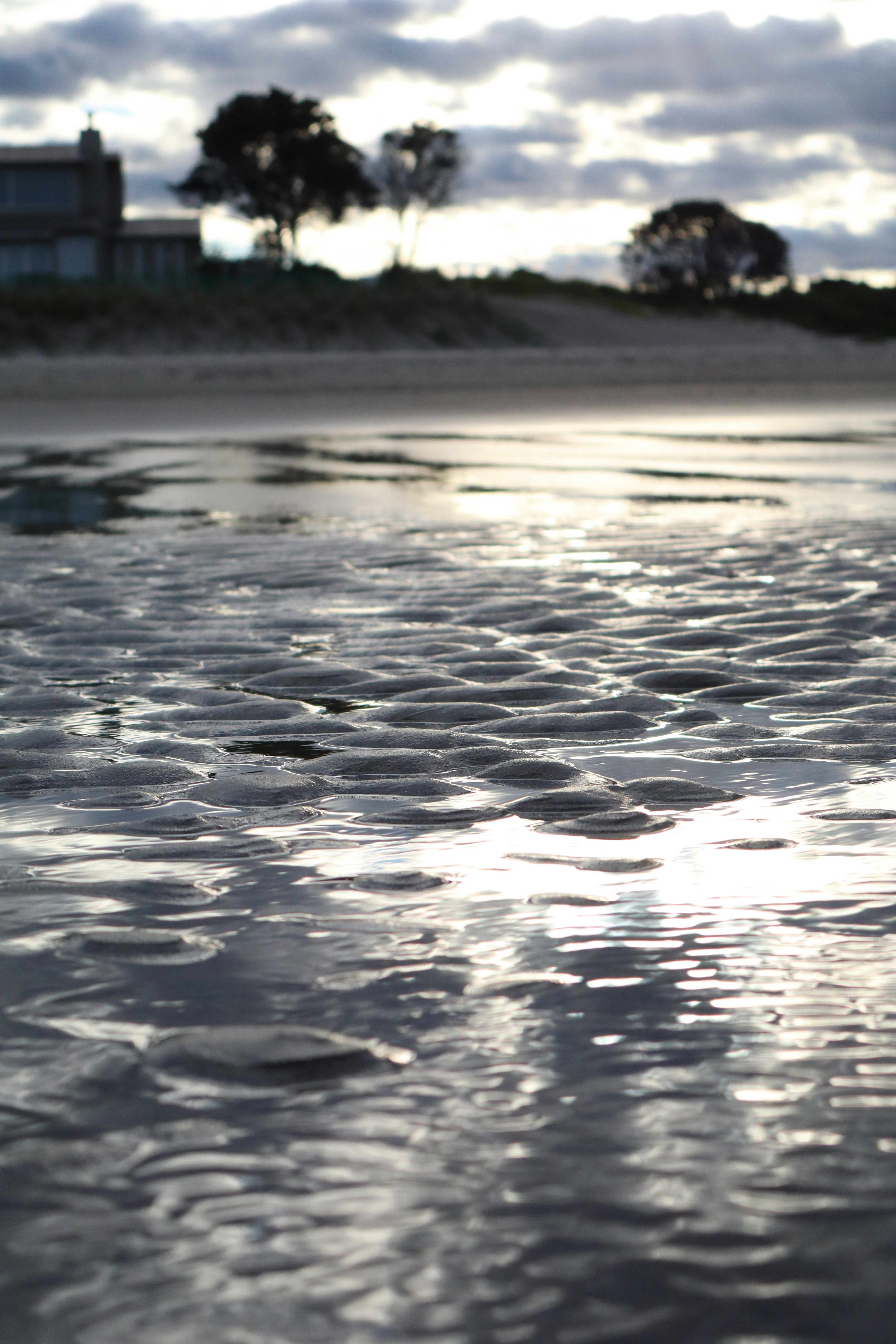 Rippled Beach at Dusk: Light Plays on Wet Sand and Silhouetted Structures