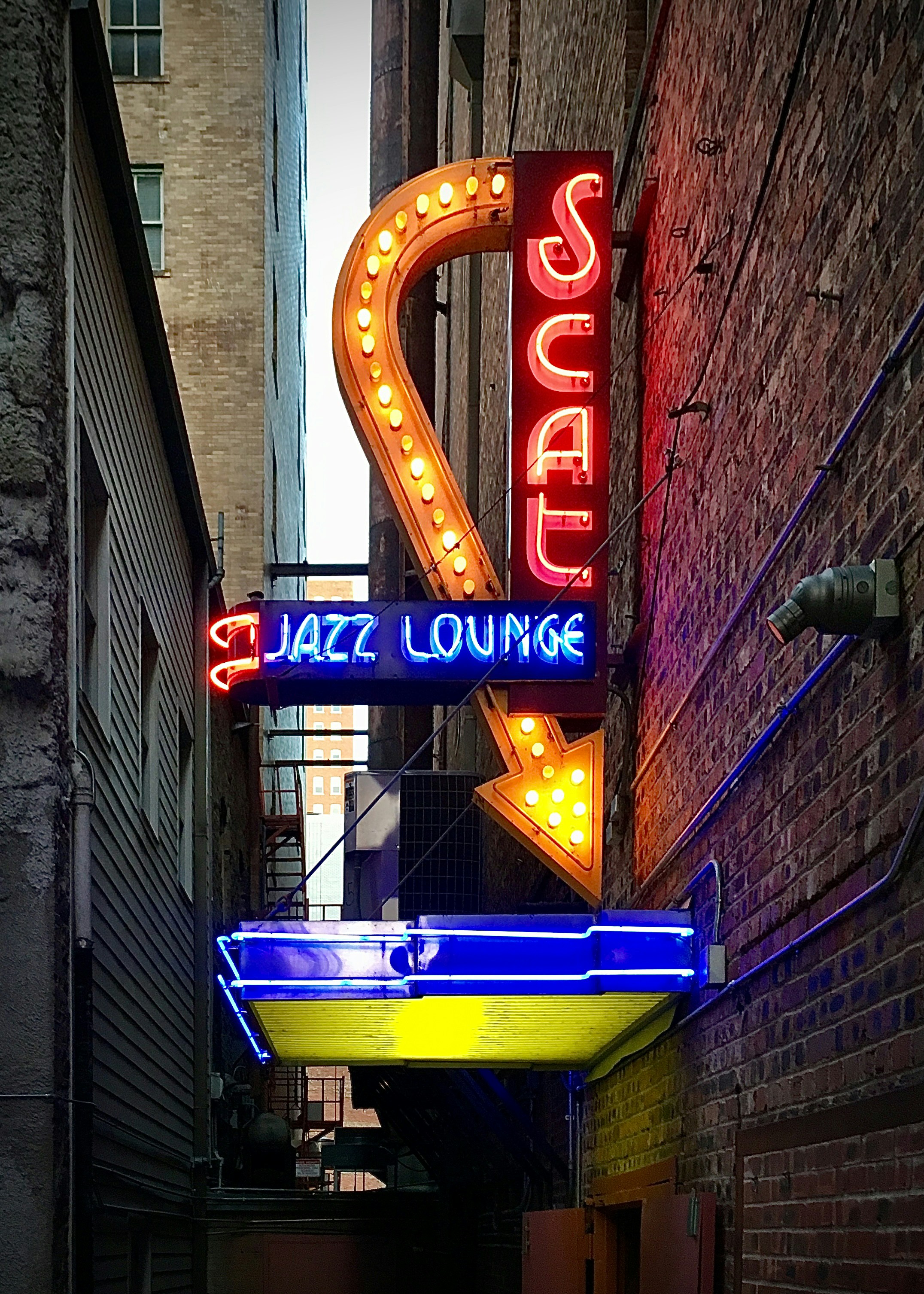Neon Alley at Scat Jazz Lounge–A glowing neon sign points the way down a narrow brick alley to Scat Jazz Lounge in Fort Worth. Bold reds, blues, and yellows cut through the urban night, capturing the hidden, after-hours energy of live jazz and classic city nightlife.